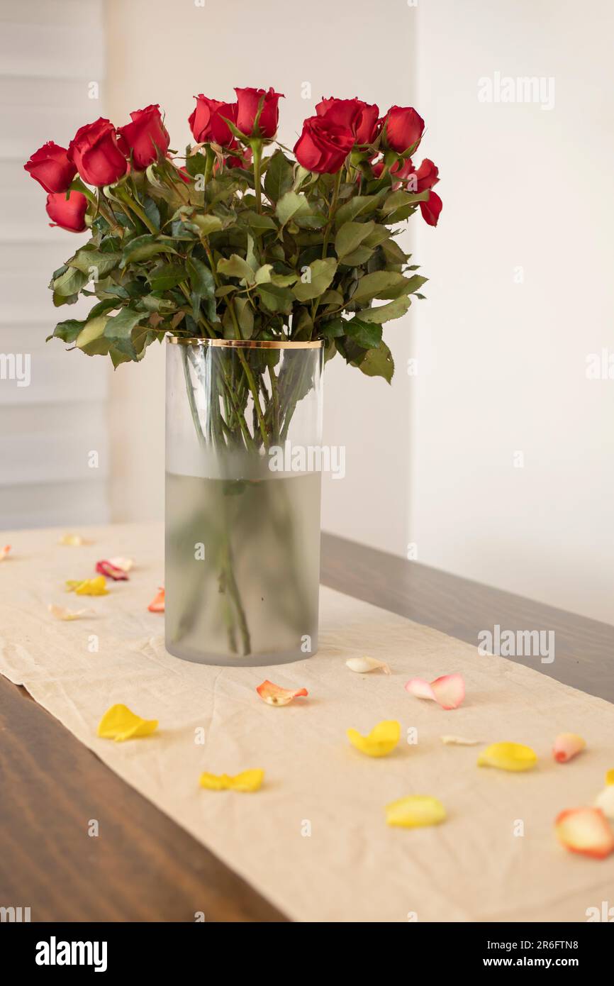 Vertical image of a vase that is on the table with a bouquet of roses ...