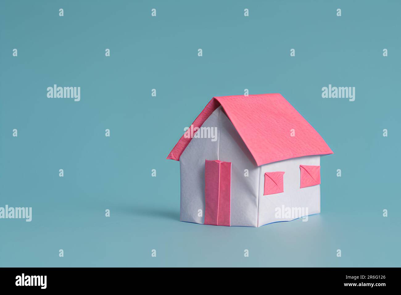 A miniature origami paper house with a pink roof against a blue ...