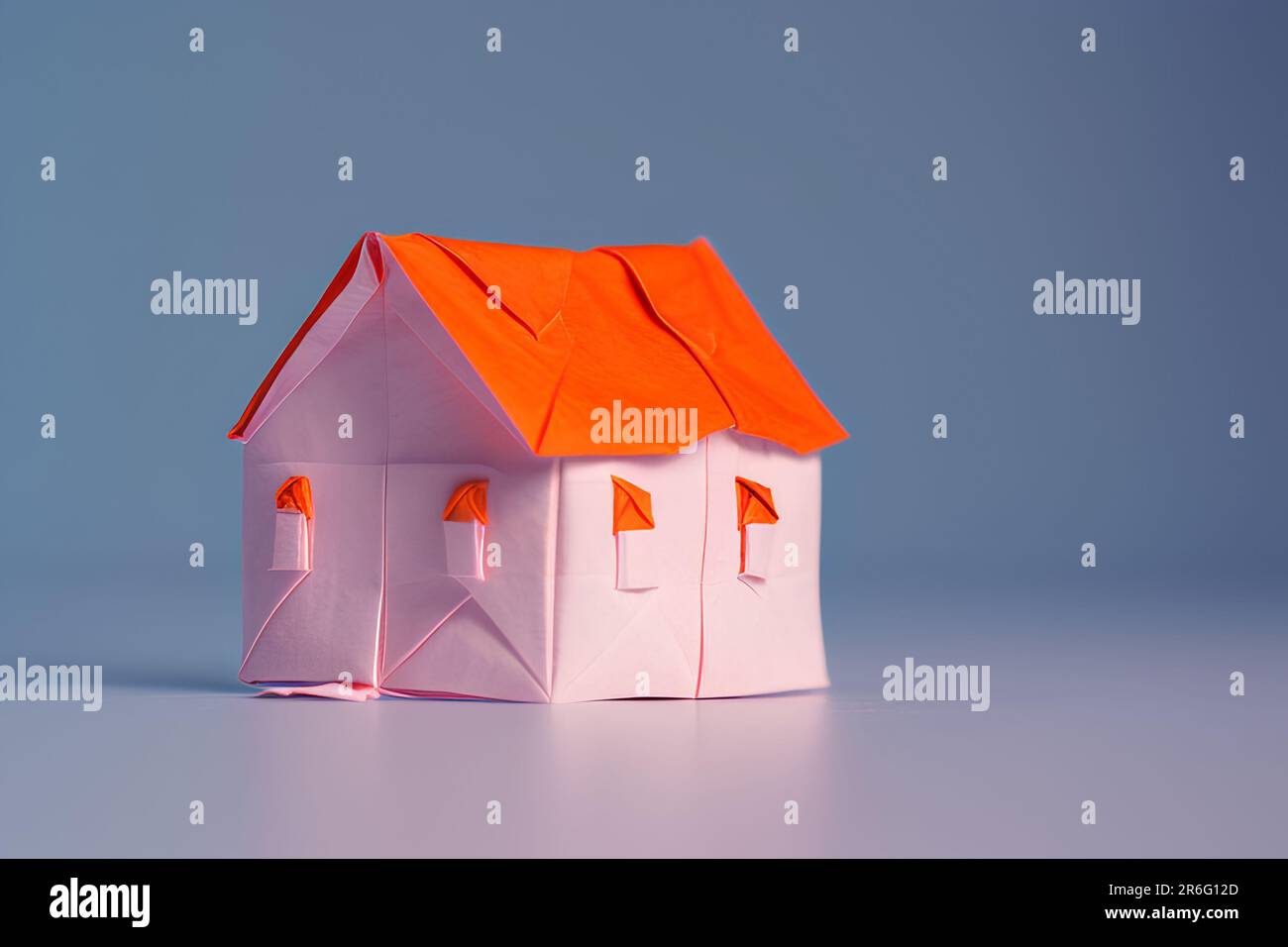 A miniature origami paper house with an orange roof against a blue ...