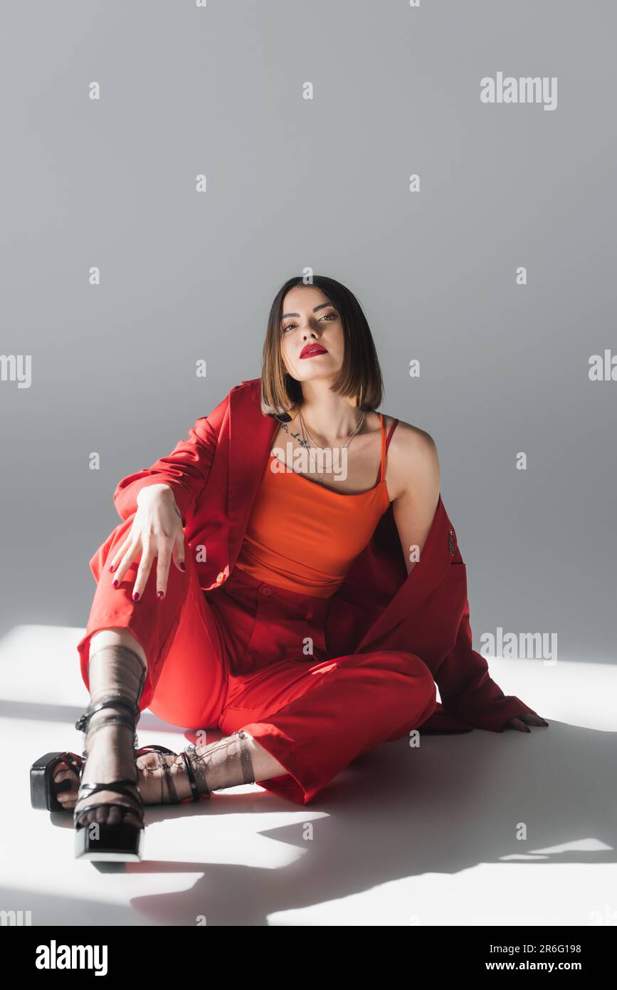 full length, young brunette woman with short hair sitting in suit on ...