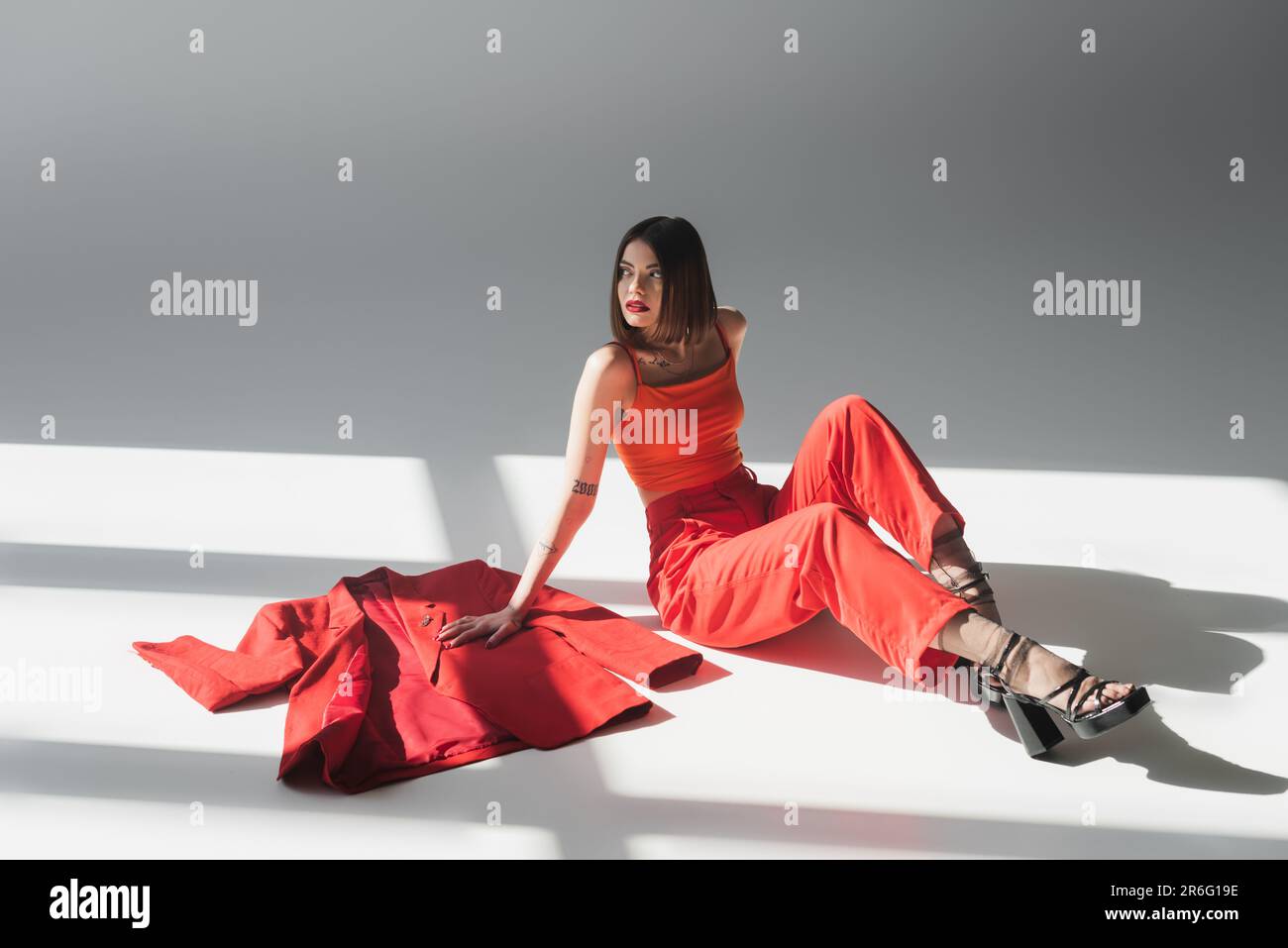 full length, young tattooed woman with short hair sitting near red ...