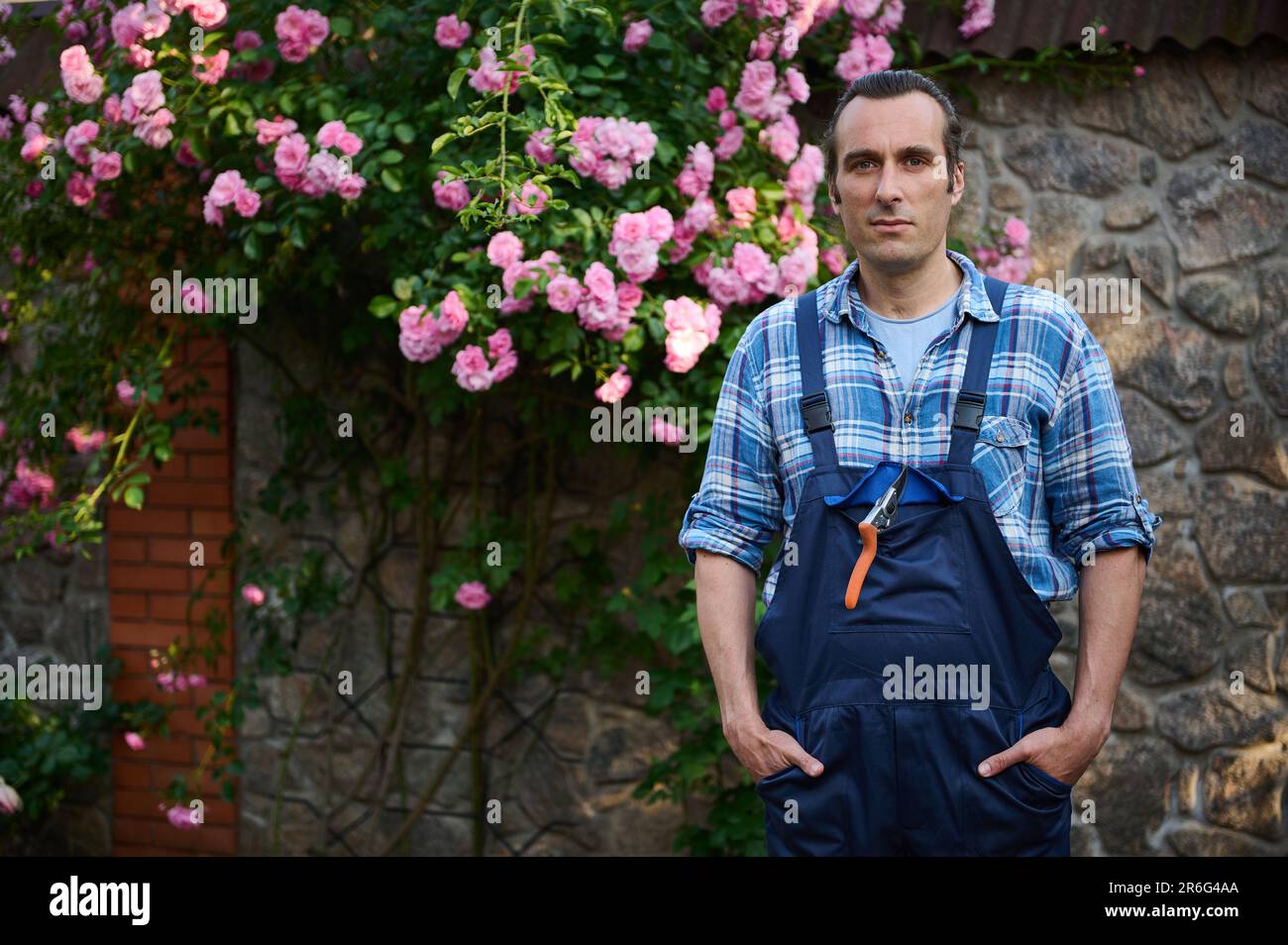 Handsome male gardener in gardening outfit, looking at camera, standing ...