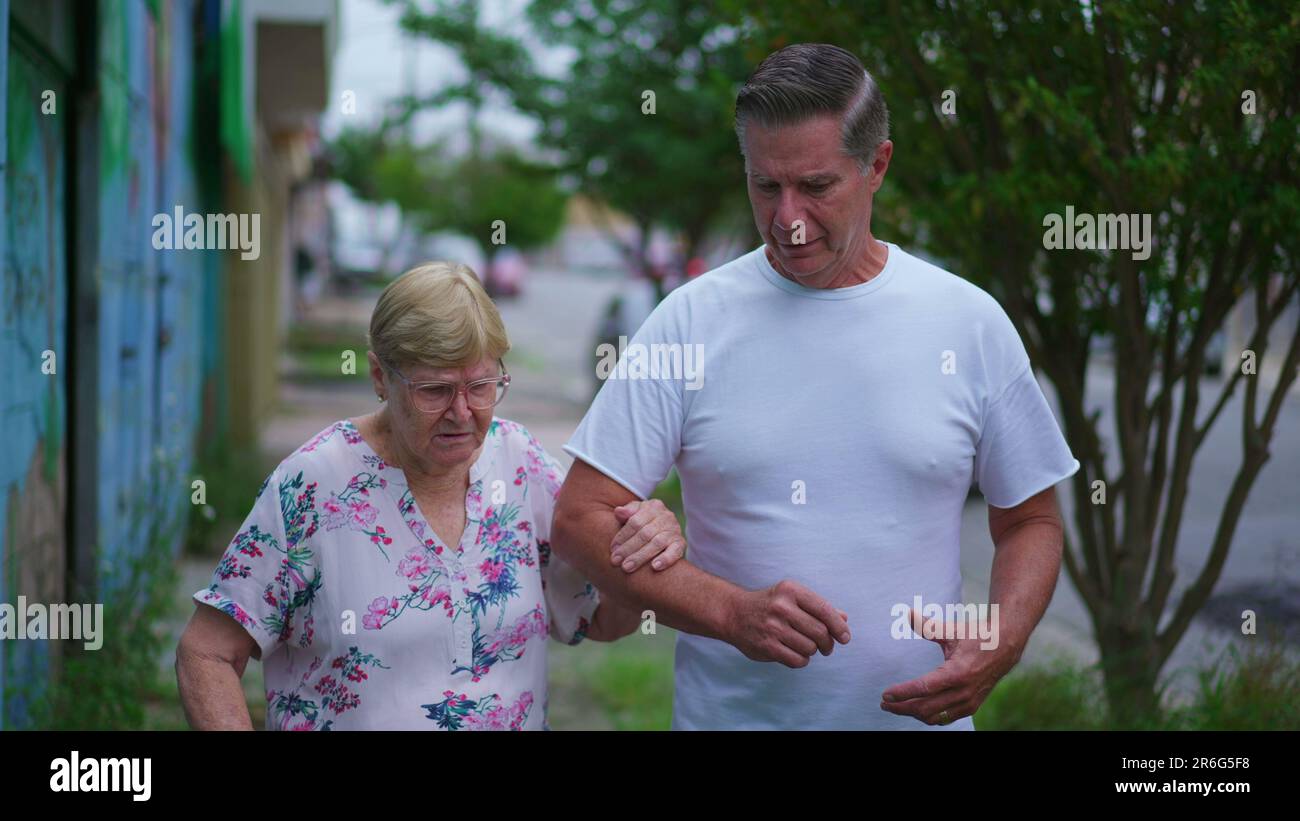 Elderly woman being helped by her adult son to walk outside. Senior 80s ...
