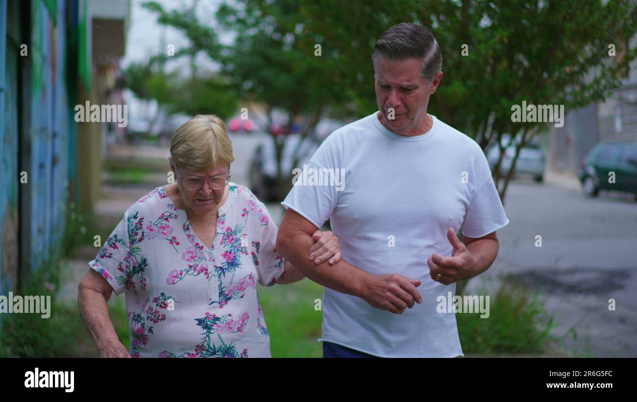 Elderly woman being helped by her adult son to walk outside. Senior 80s ...