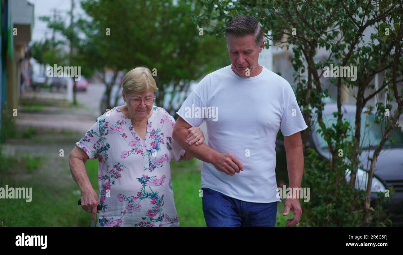 Elderly woman being helped by her adult son to walk outside. Senior 80s ...