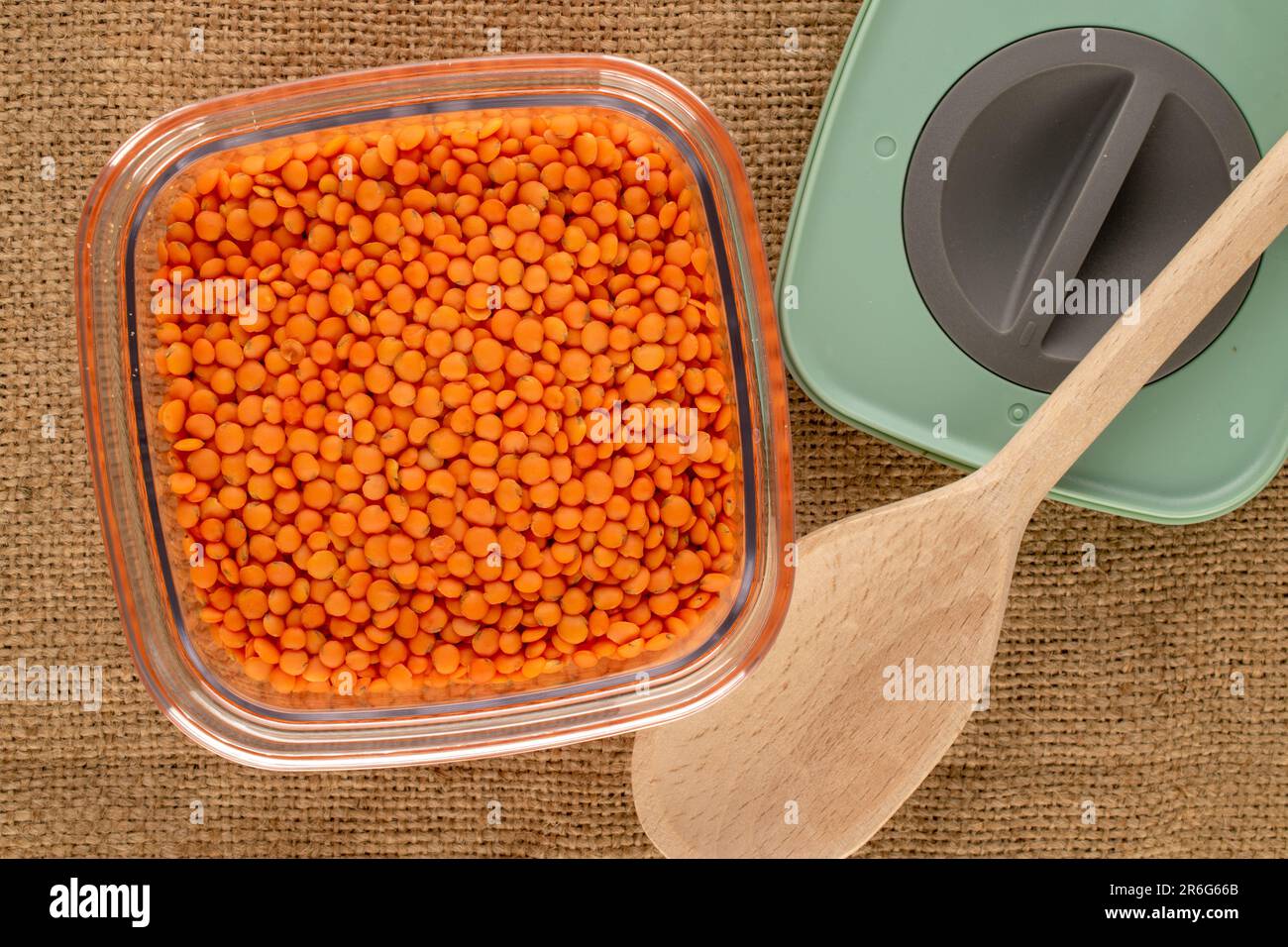 Red lentils in plastic container with wooden spoon on jute cloth, macro ...