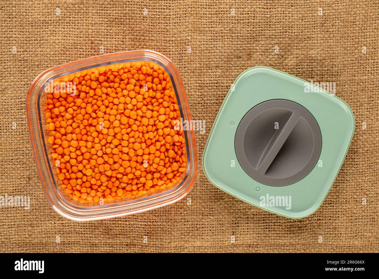 Red lentils in a plastic container on a jute cloth, macro, top view ...