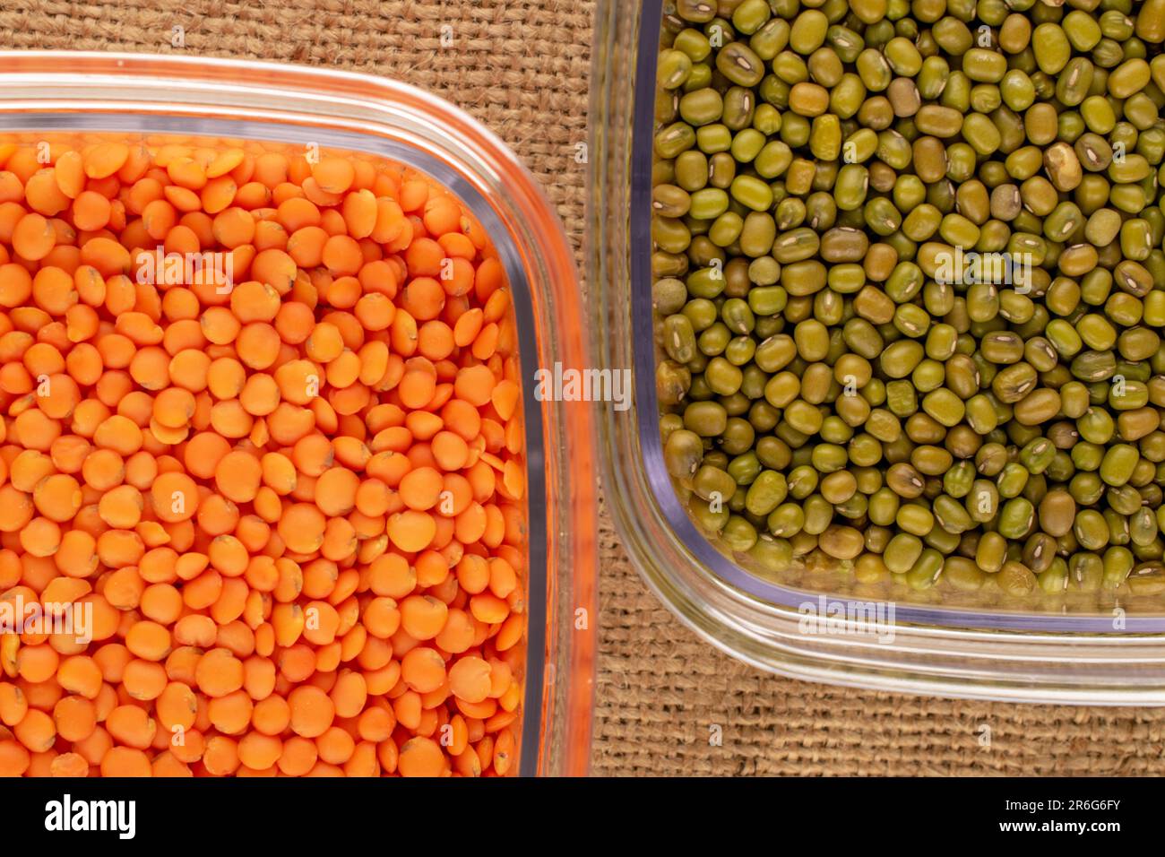 Red lentils and mung beans in plastic containers on jute cloth, macro ...