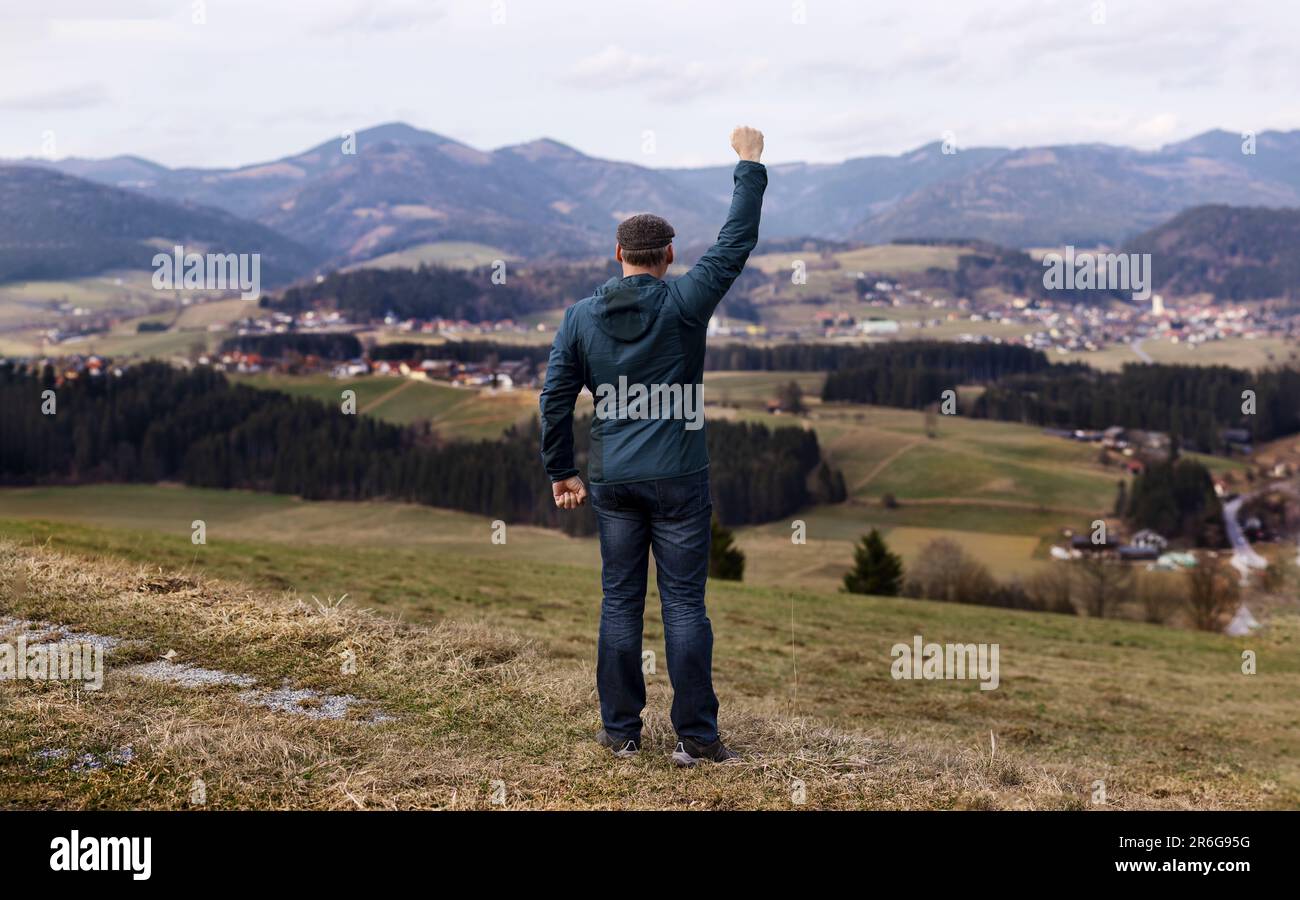 a man waves his hand, standing on a hill against the beautiful alpine ...