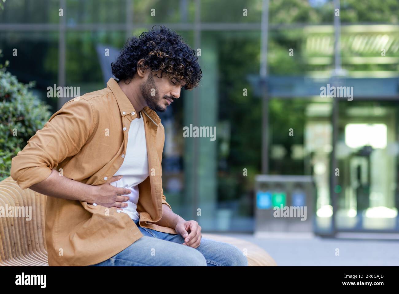 A young Hispanic man is sitting on a bench outside and holding his ...
