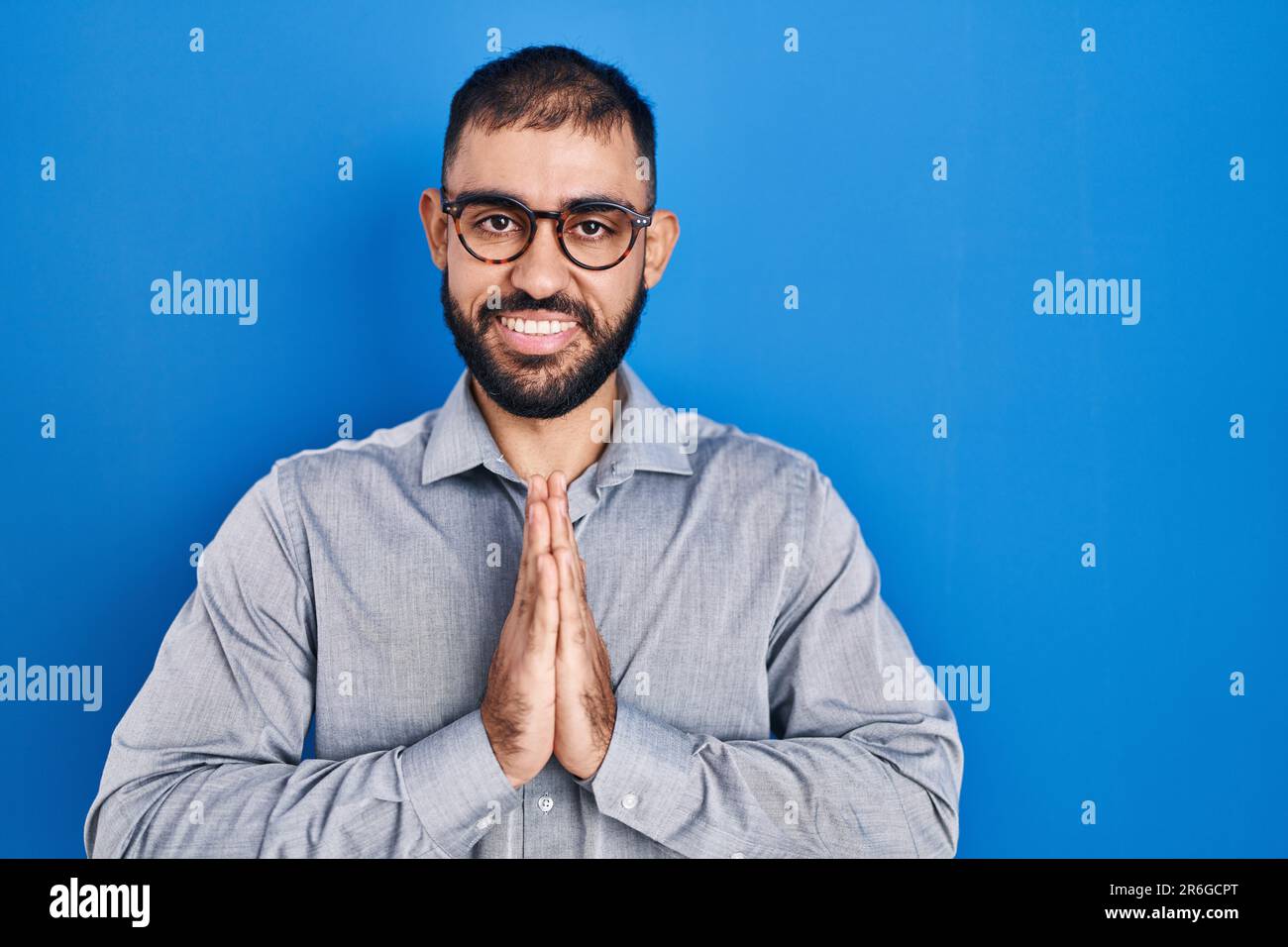 Middle east man with beard standing over blue background praying with ...