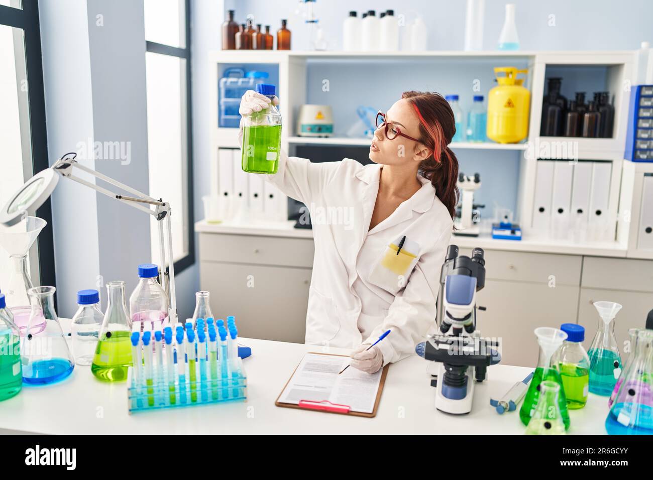 Young caucasian woman scientist measuring liquid writing on document at ...