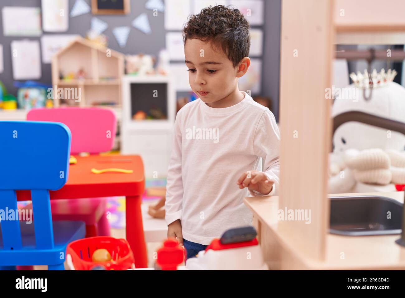 Adorable hispanic boy playing supermarket game standing at kindergarten ...