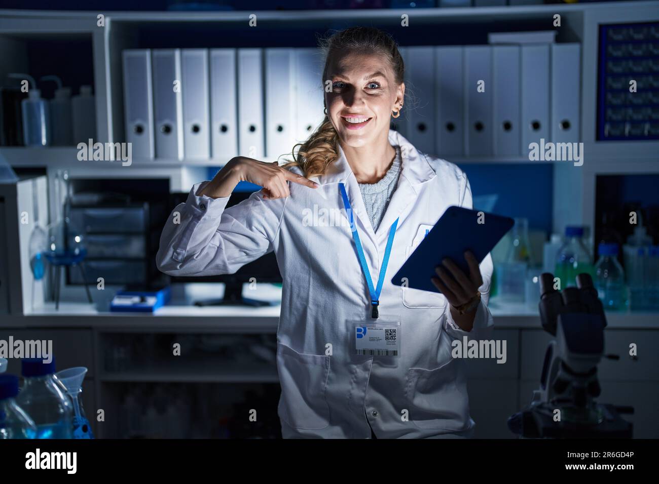 Beautiful blonde woman working at scientist laboratory late at night looking confident with ...