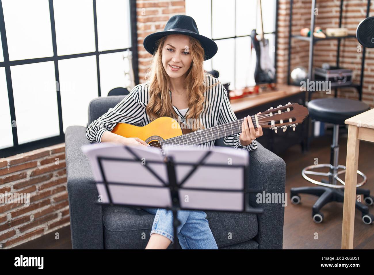 Young blonde woman musician playing classical guitar at music studio ...