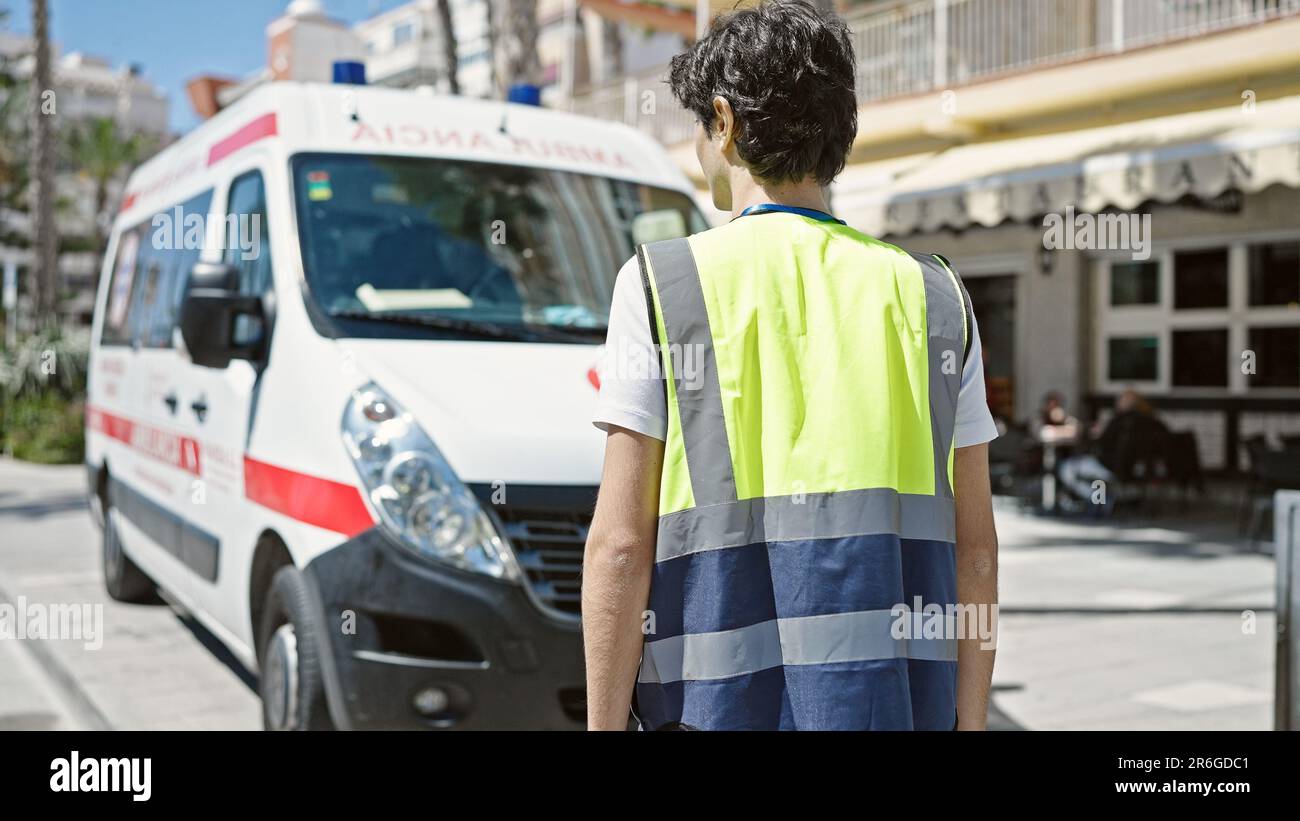 Young hispanic man nurse standing by ambulance backwards at street ...