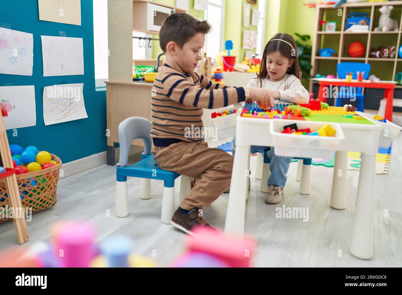 Adorable boy and girl playing with construction blocks sitting on table ...