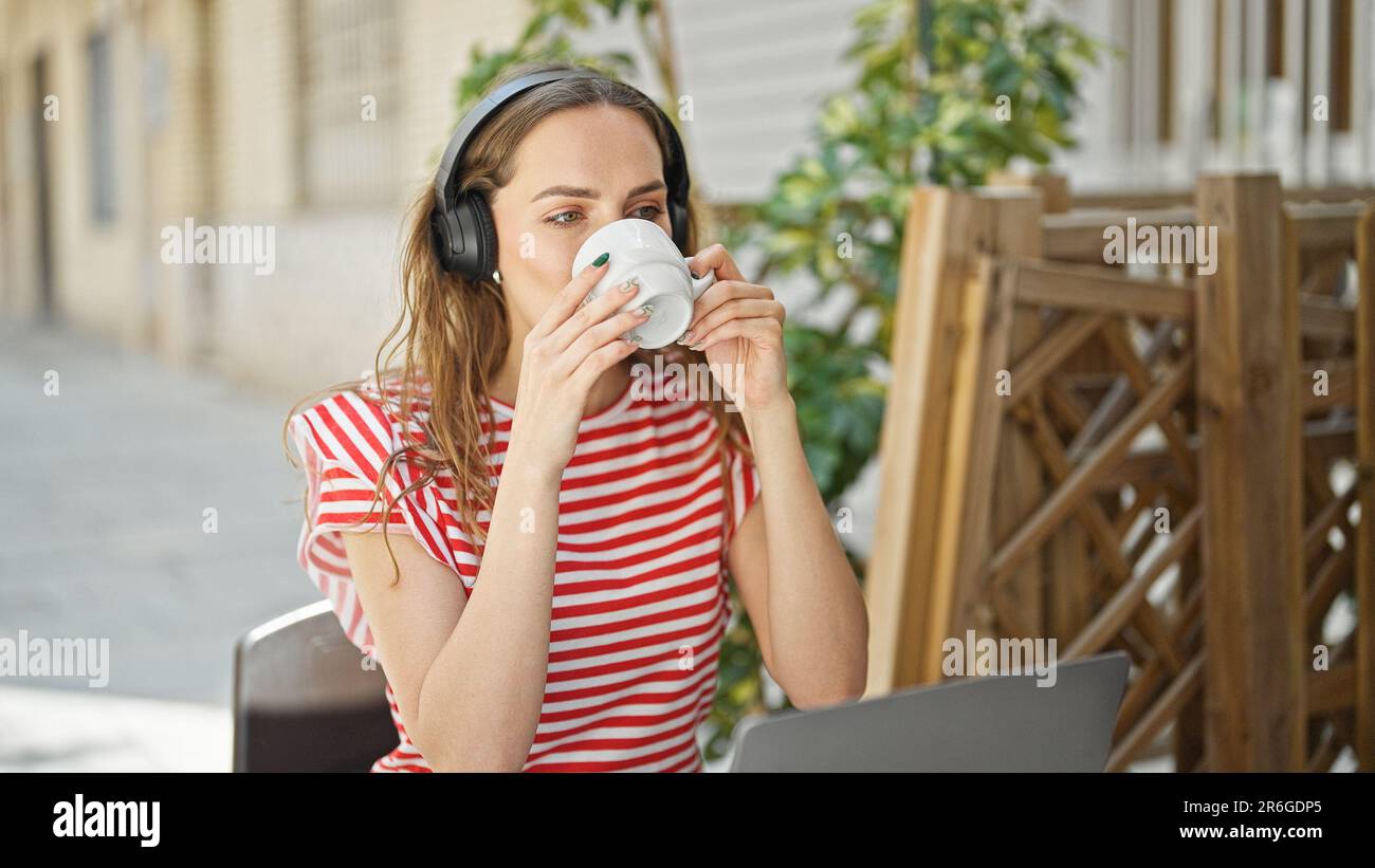 Young blonde woman listening to music drinking coffee at coffee shop ...