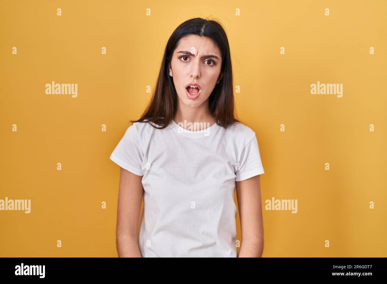 Young beautiful woman standing over yellow background in shock face ...