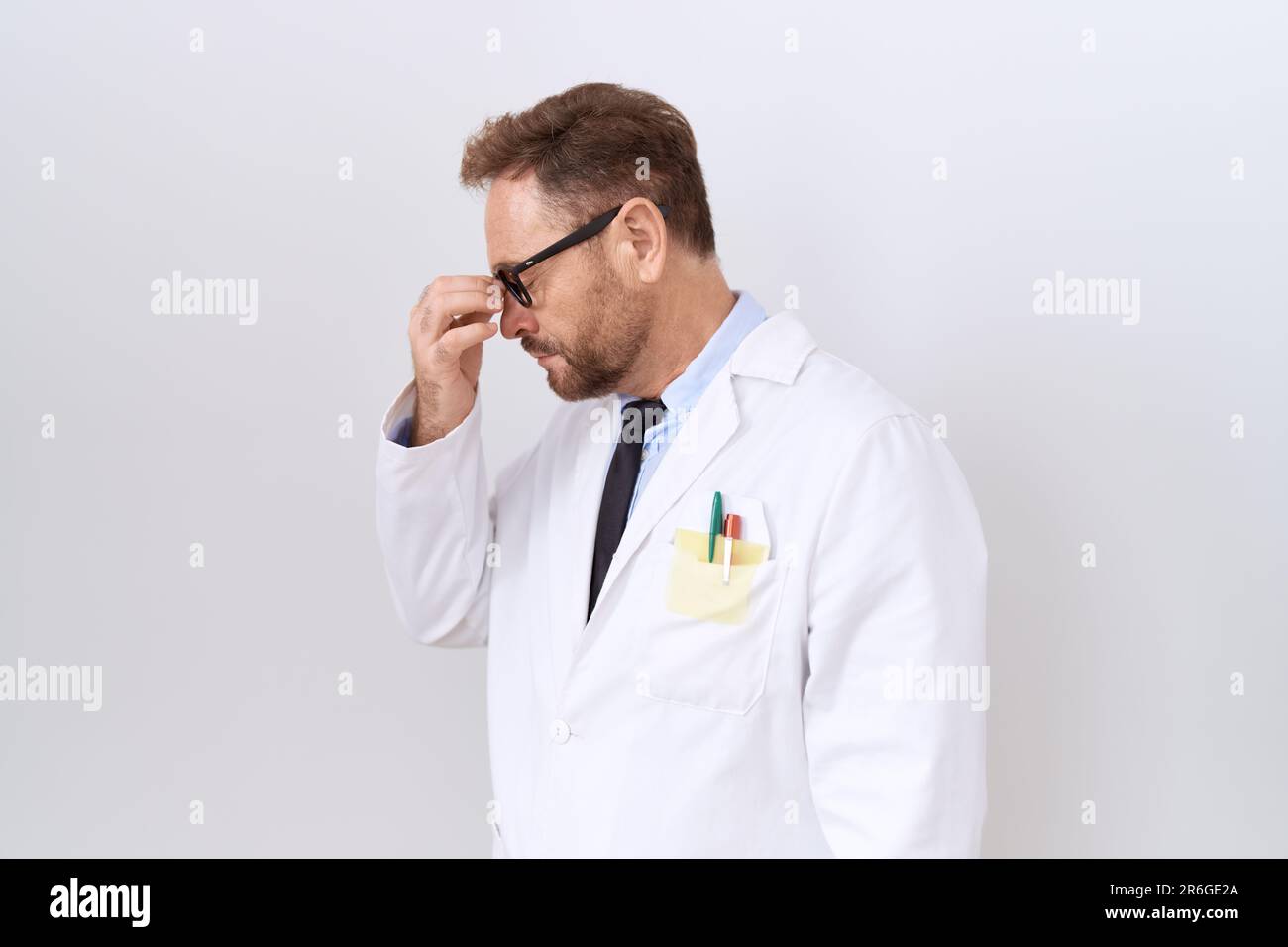 Middle age doctor man with beard wearing white coat tired rubbing nose ...