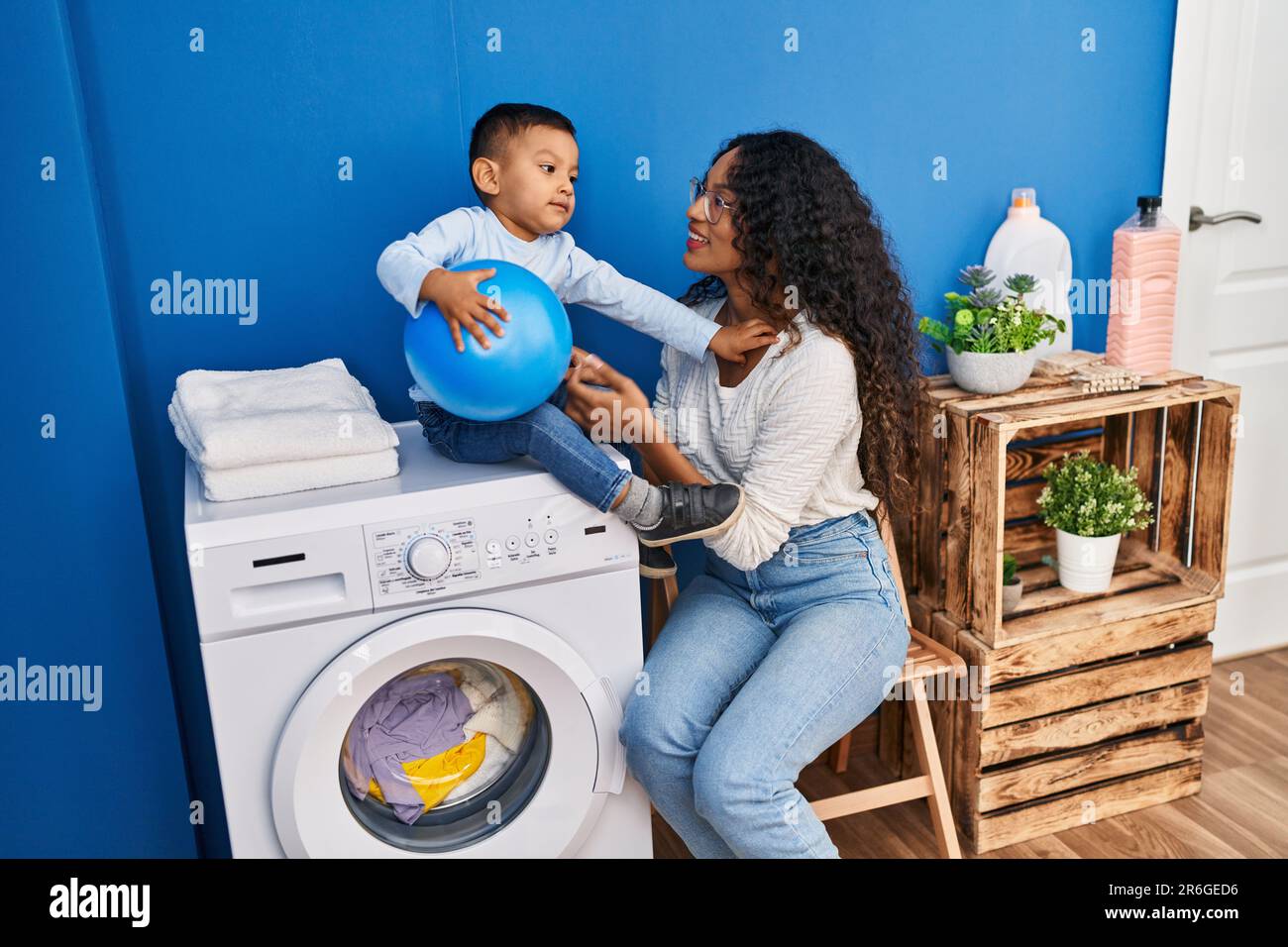 Mother and son playing with ball waiting for washing machine at laundry ...