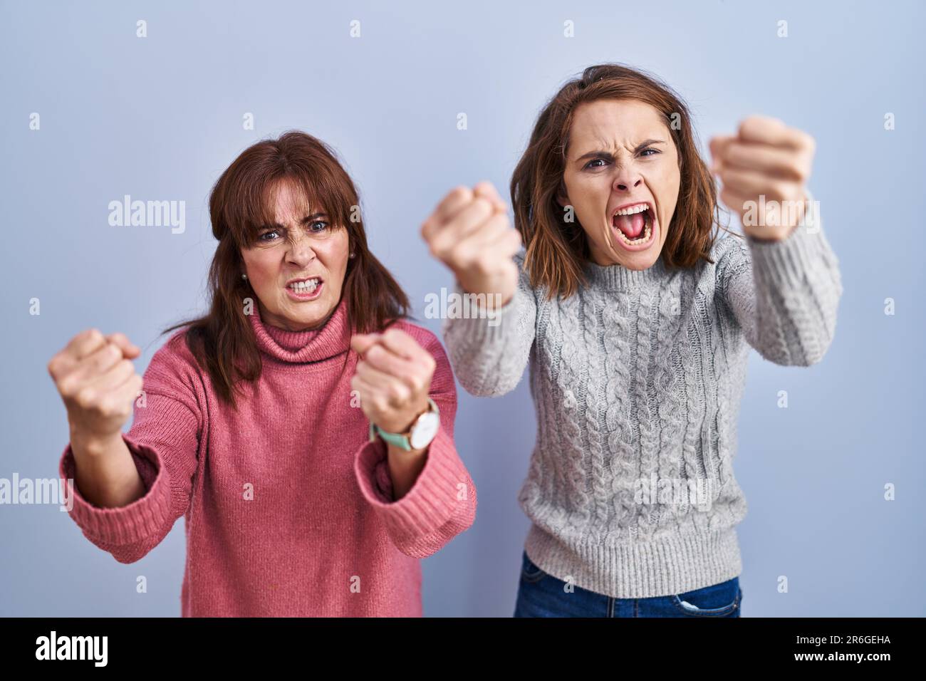 Mother and daughter standing over blue background angry and mad raising ...