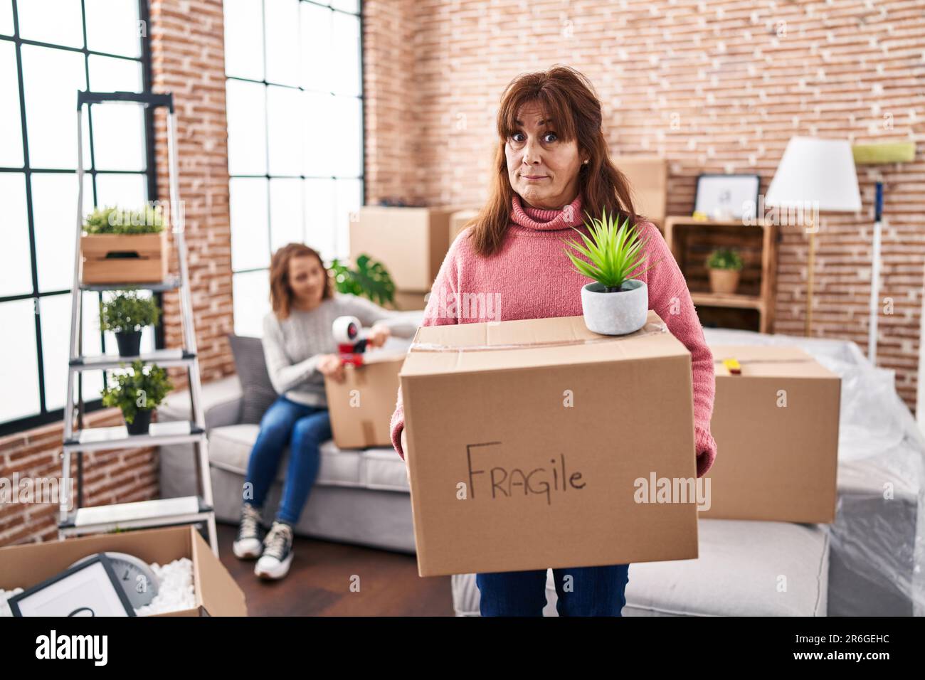 Mother and daughter moving to a new home holding cardboard box skeptic ...