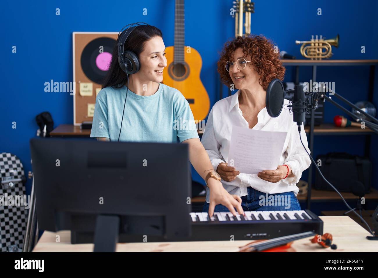 Two women musicians singing song playing piano keyboard at music studio ...