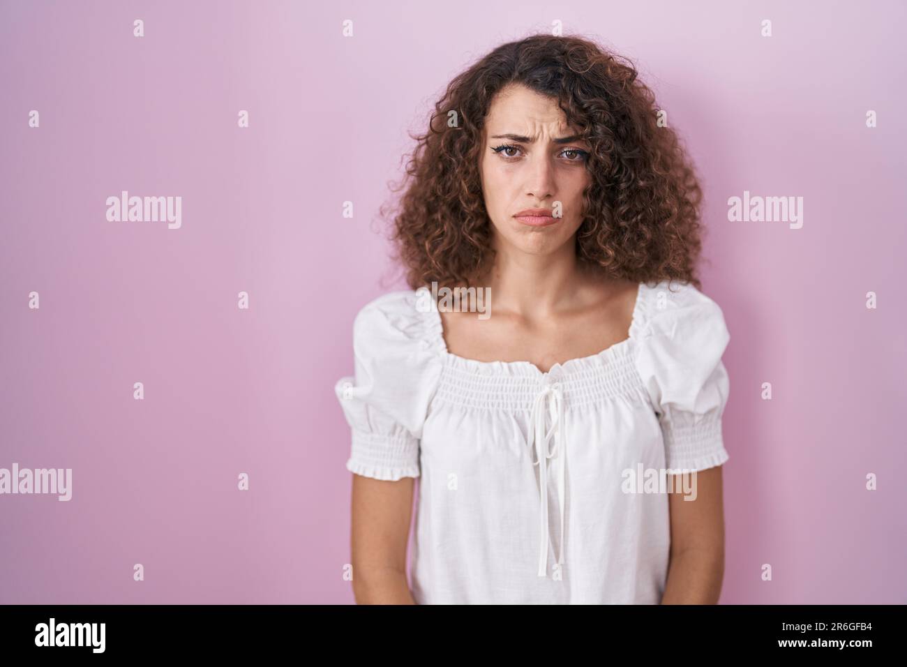 Hispanic woman with curly hair standing over pink background depressed ...