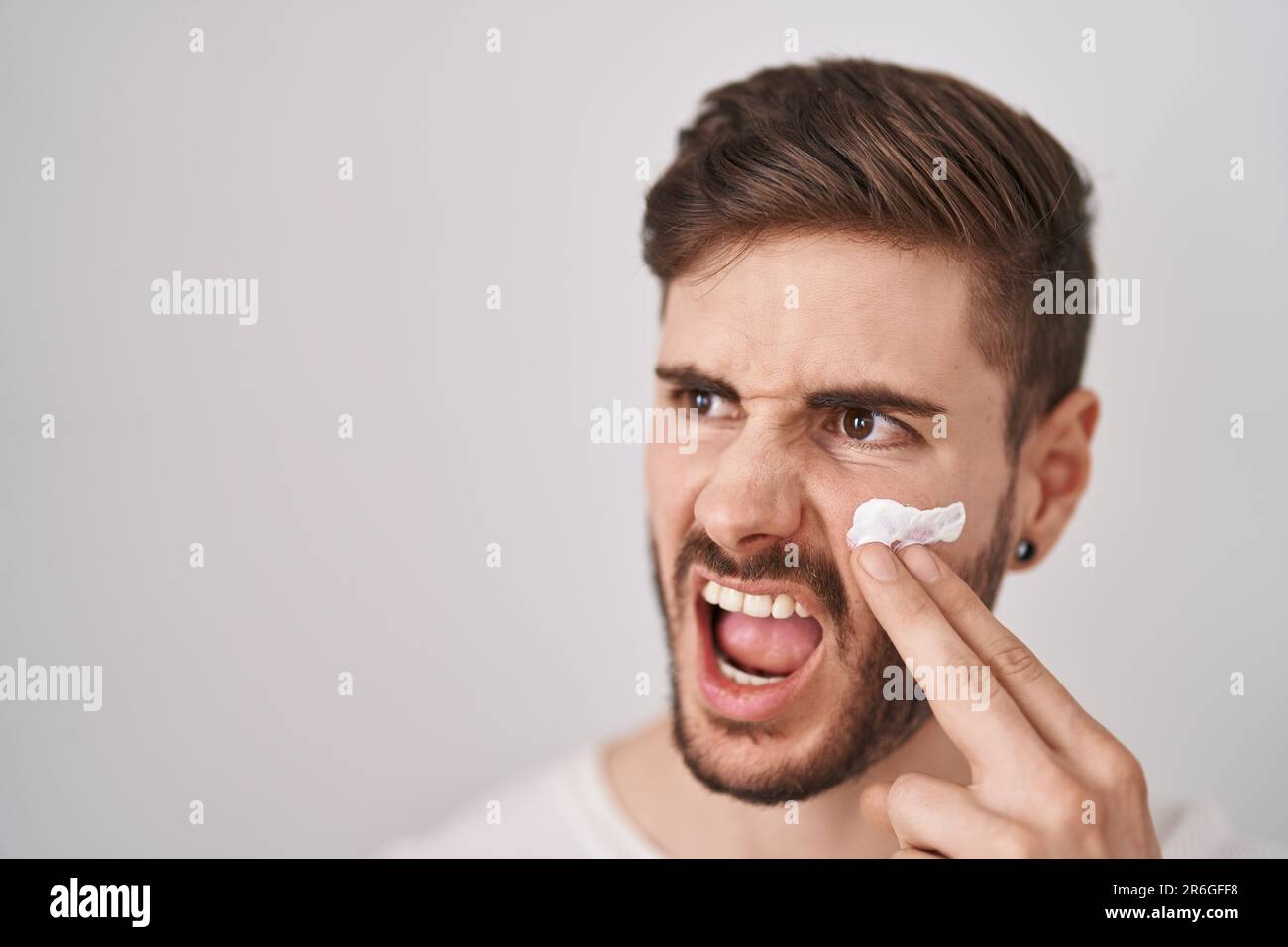 Hispanic man with beard using moisturizer facial cream angry and mad ...
