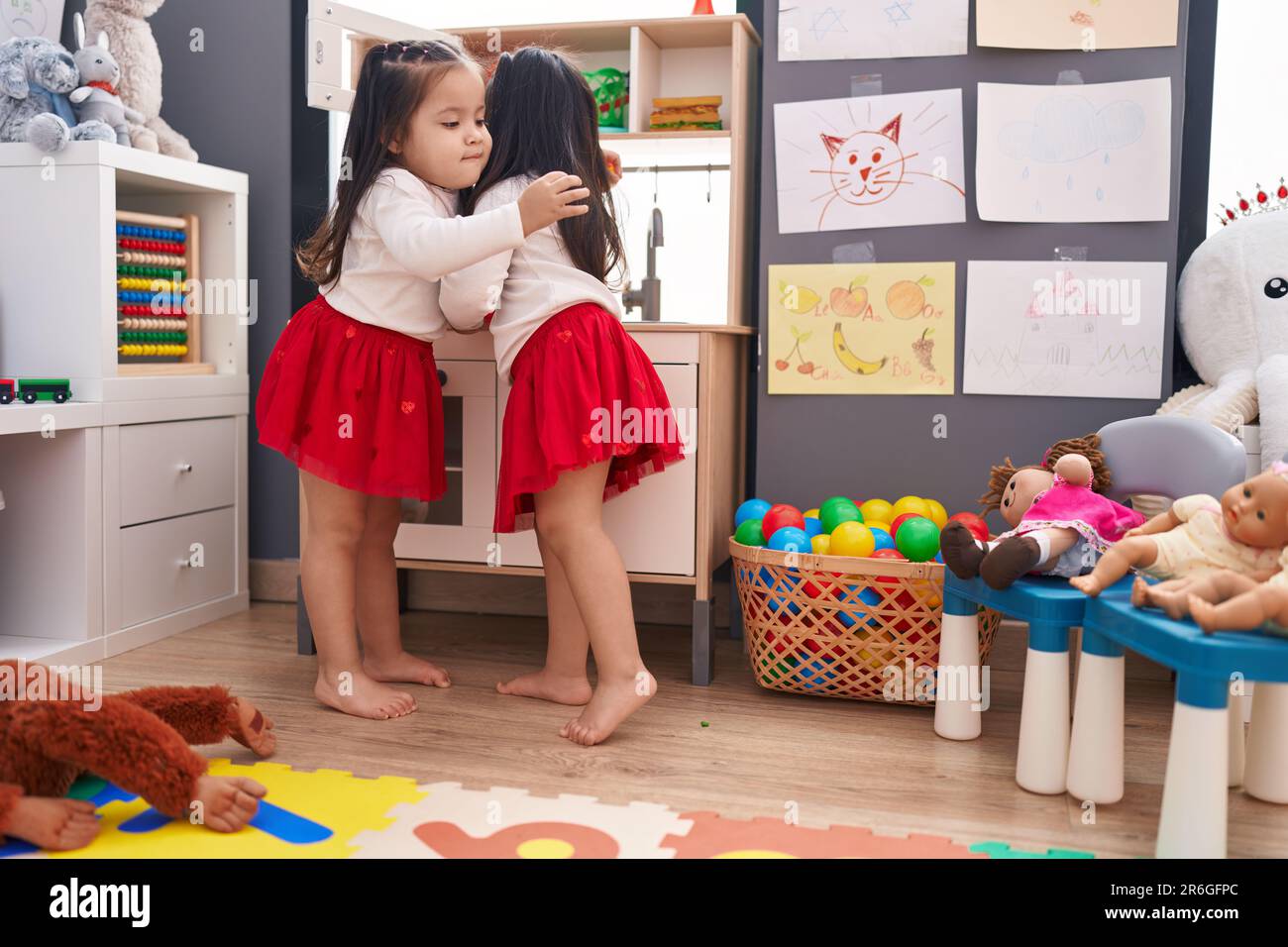 Adorable twin girls playing with play kitchen hugging each other at ...