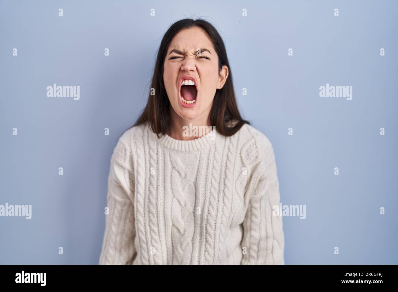 Young brunette woman standing over blue background angry and mad ...