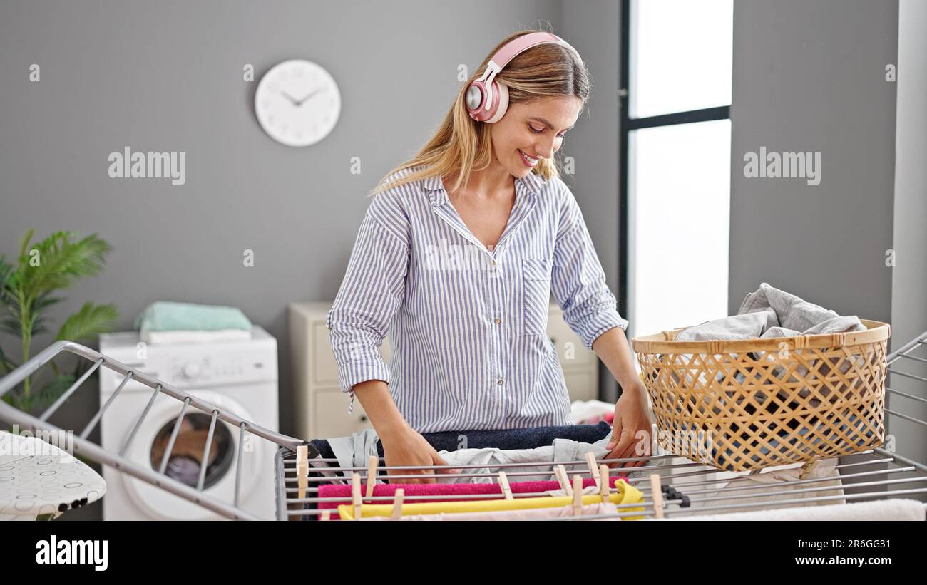 Young blonde woman listening to music hanging clothes on clothesline at ...