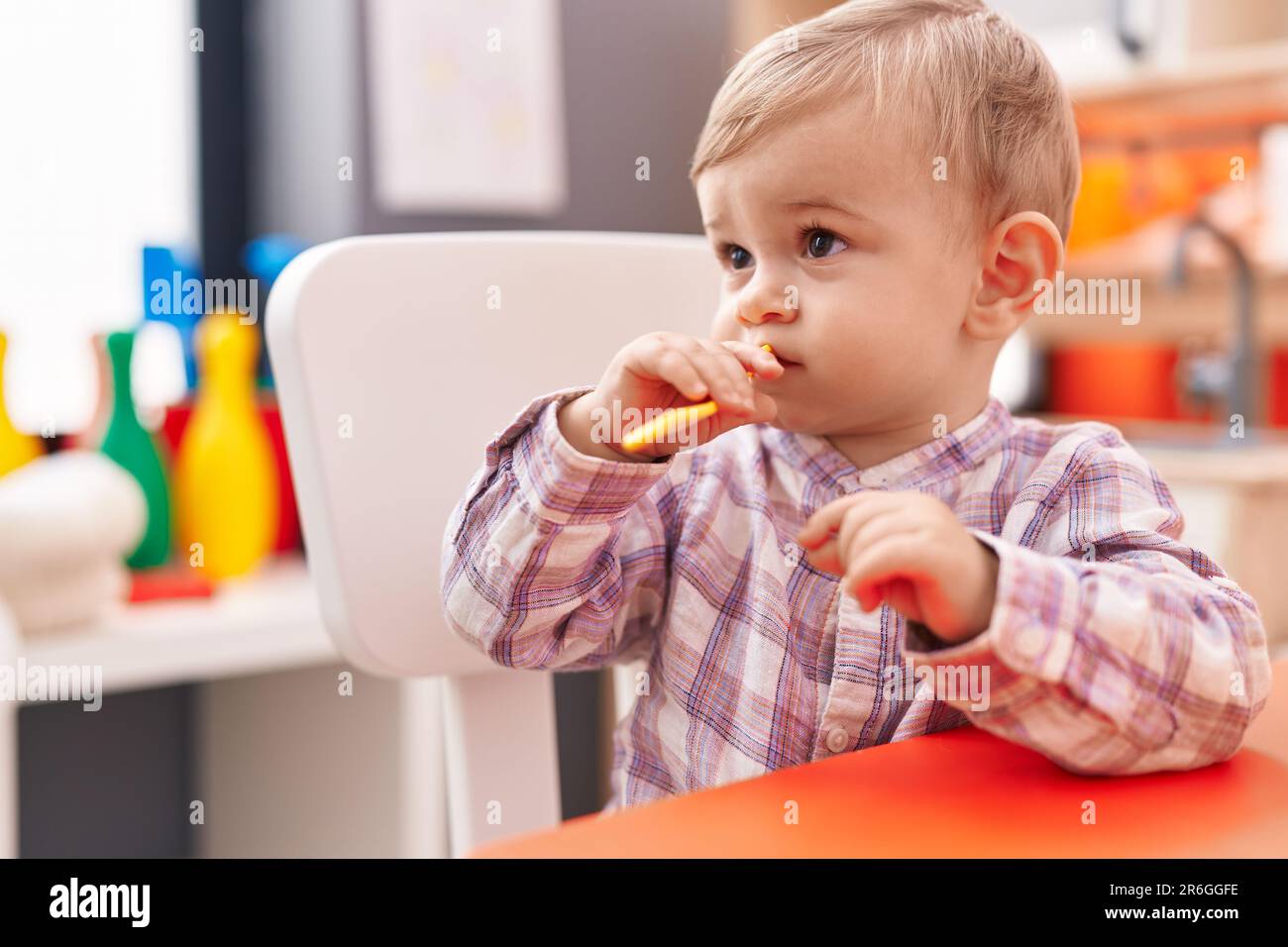 Adorable caucasian boy sitting on table sucking spoon at kindergarten ...