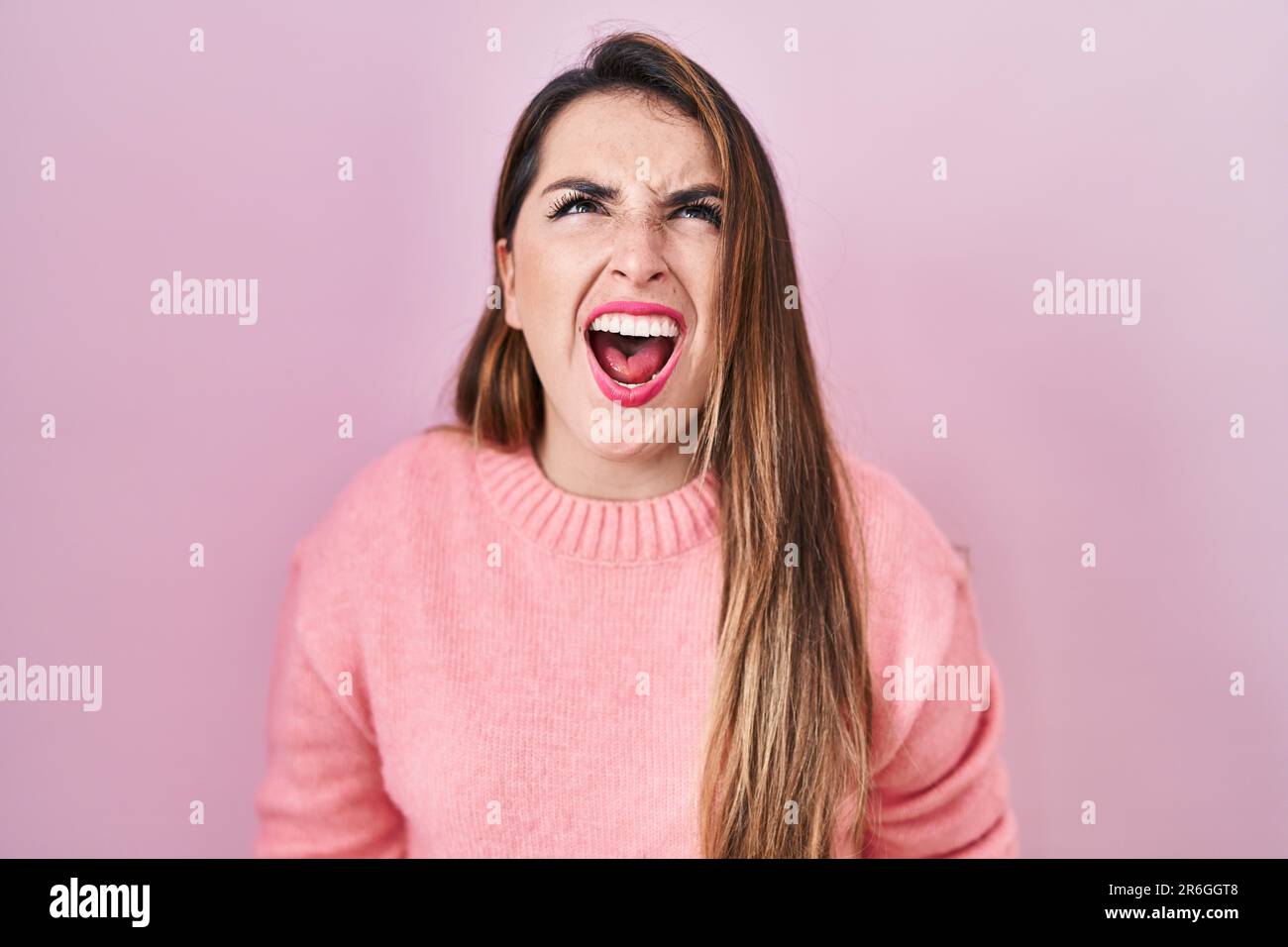 Young hispanic woman standing over pink background angry and mad ...