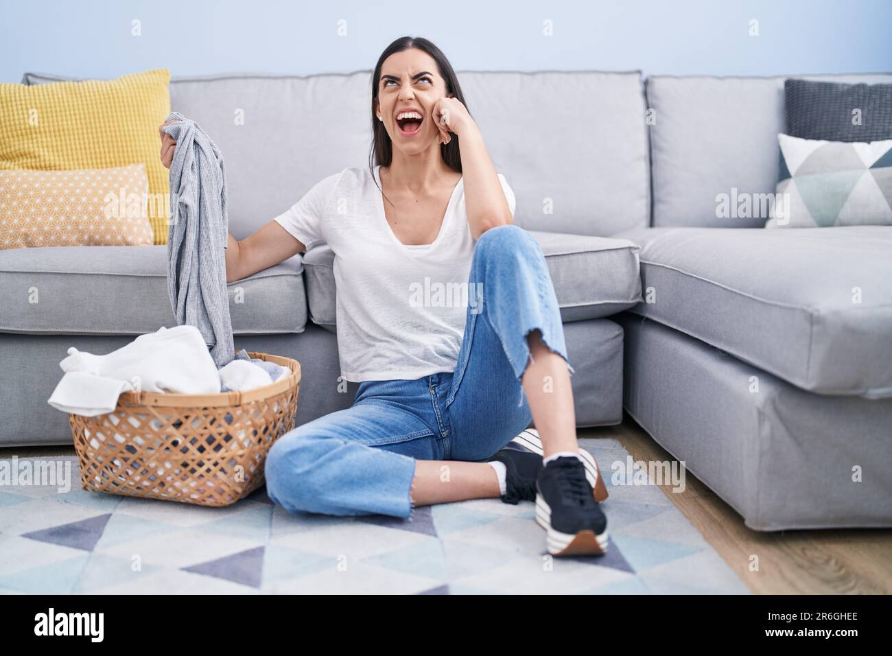 Young brunette woman doing laundry at home angry and mad screaming ...