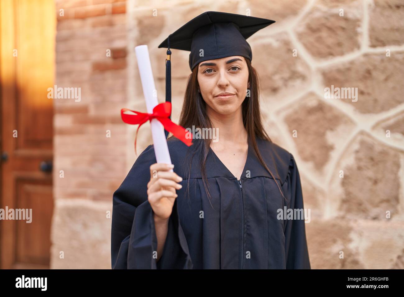 Young hispanic woman wearing graduated uniform holding diploma at ...