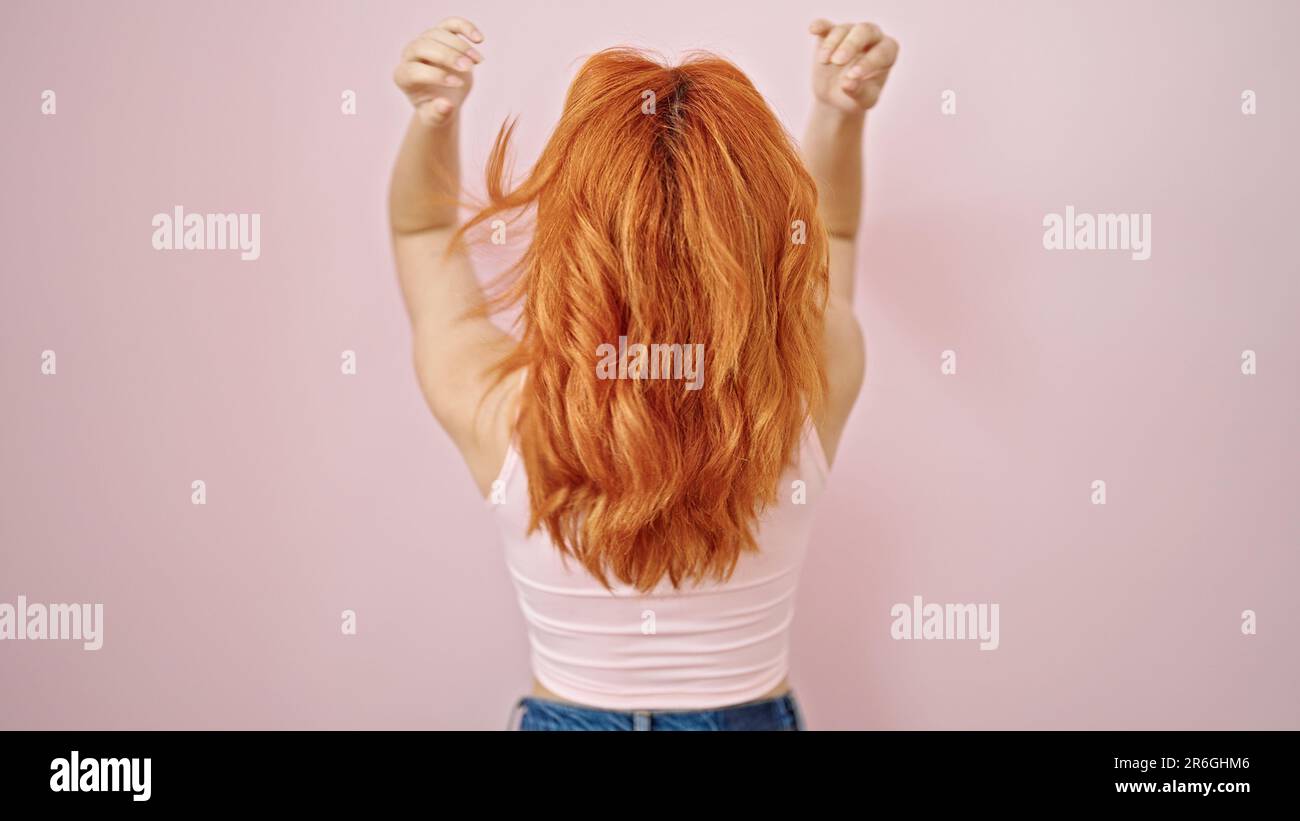 Young redhead woman touching her hair backwards over isolated pink ...