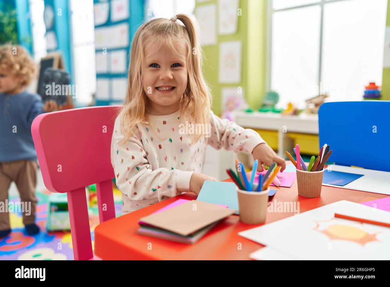 Adorable boy and girl student cutting paper sitting on table at ...
