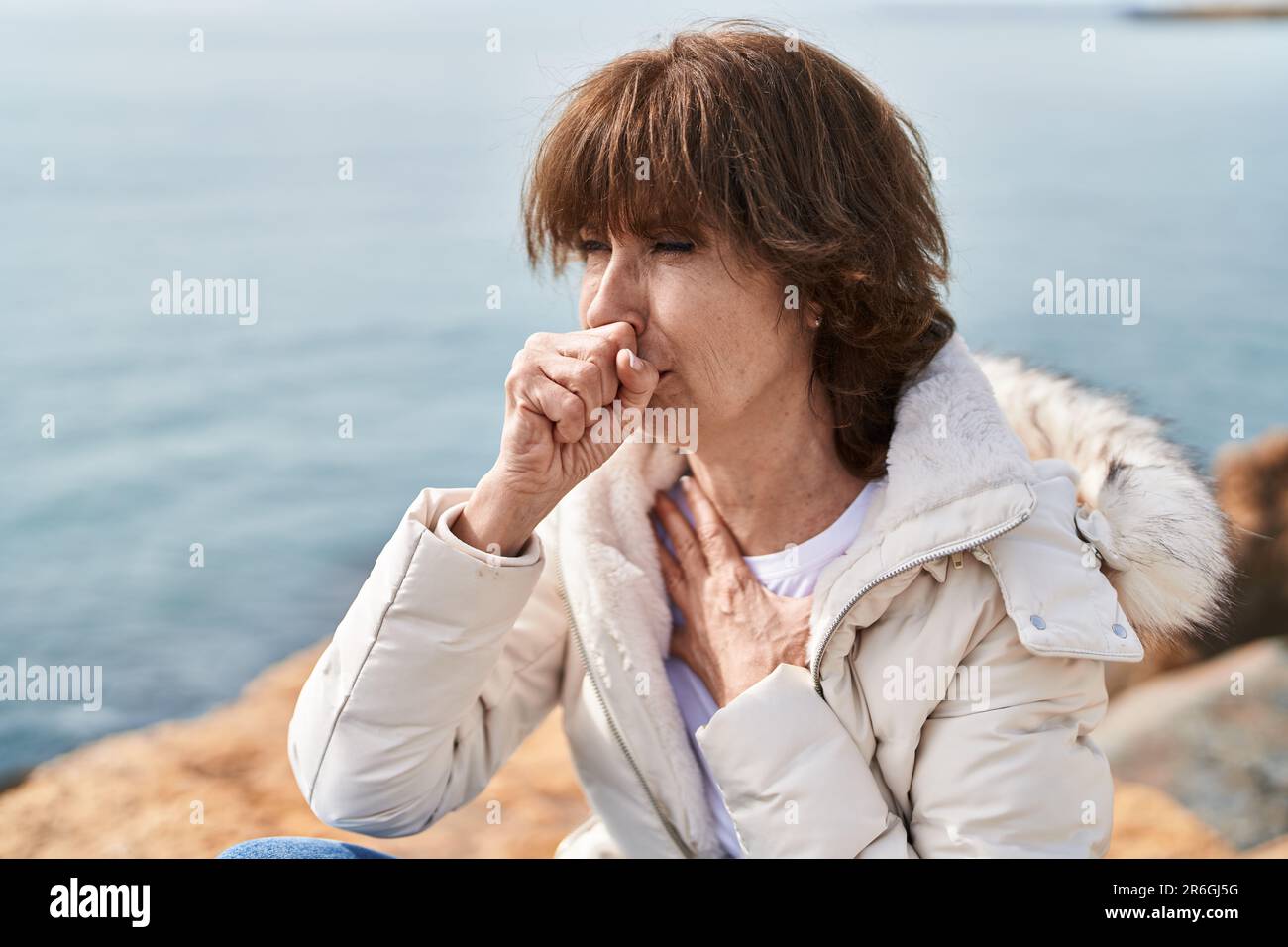 Middle age woman coughing sitting on the rock at seaside Stock Photo ...