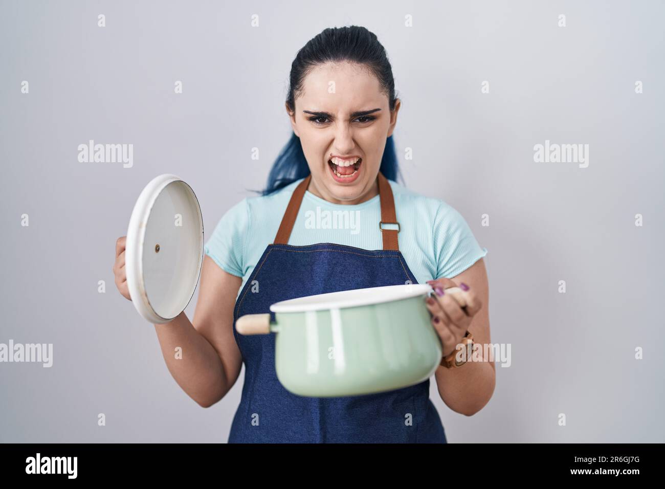 Young modern girl with blue hair wearing apron holding cooking pot ...