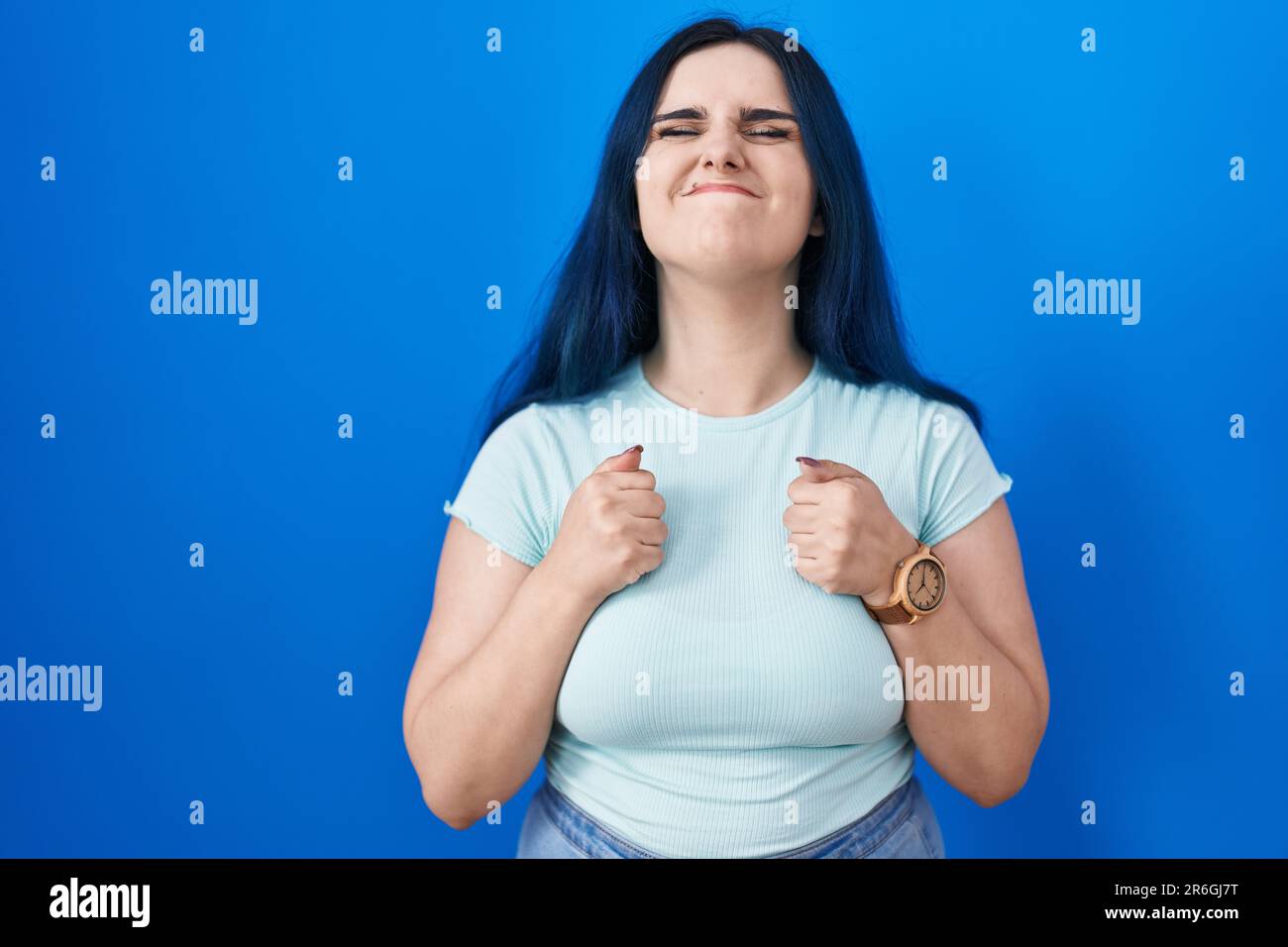 Young modern girl with blue hair standing over blue background excited ...