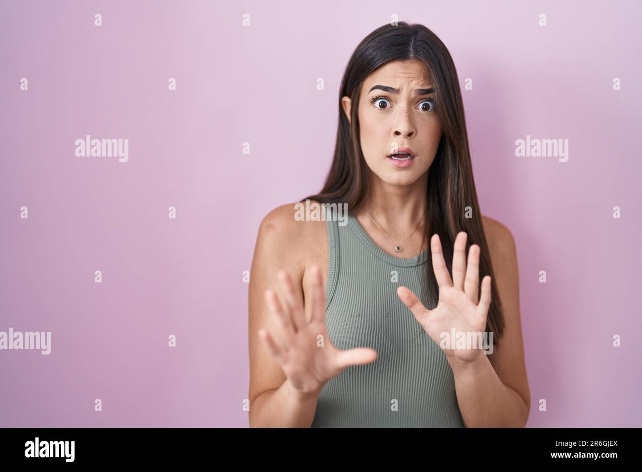 Hispanic woman standing over pink background afraid and terrified with ...