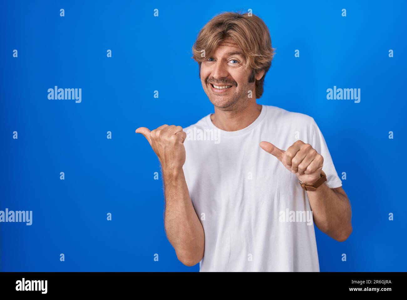 Middle age man standing over blue background pointing to the back ...