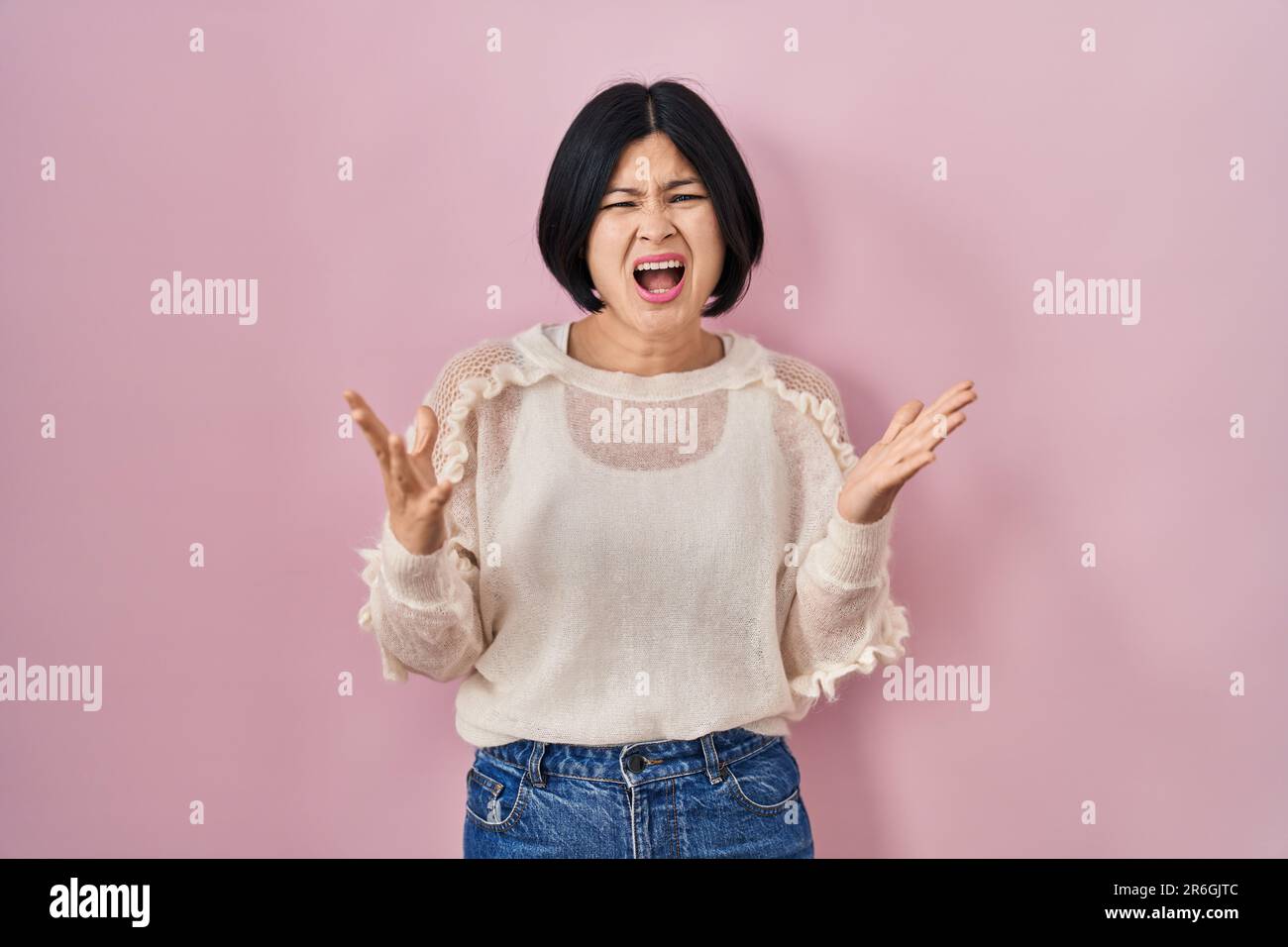 Young asian woman standing over pink background crazy and mad shouting ...