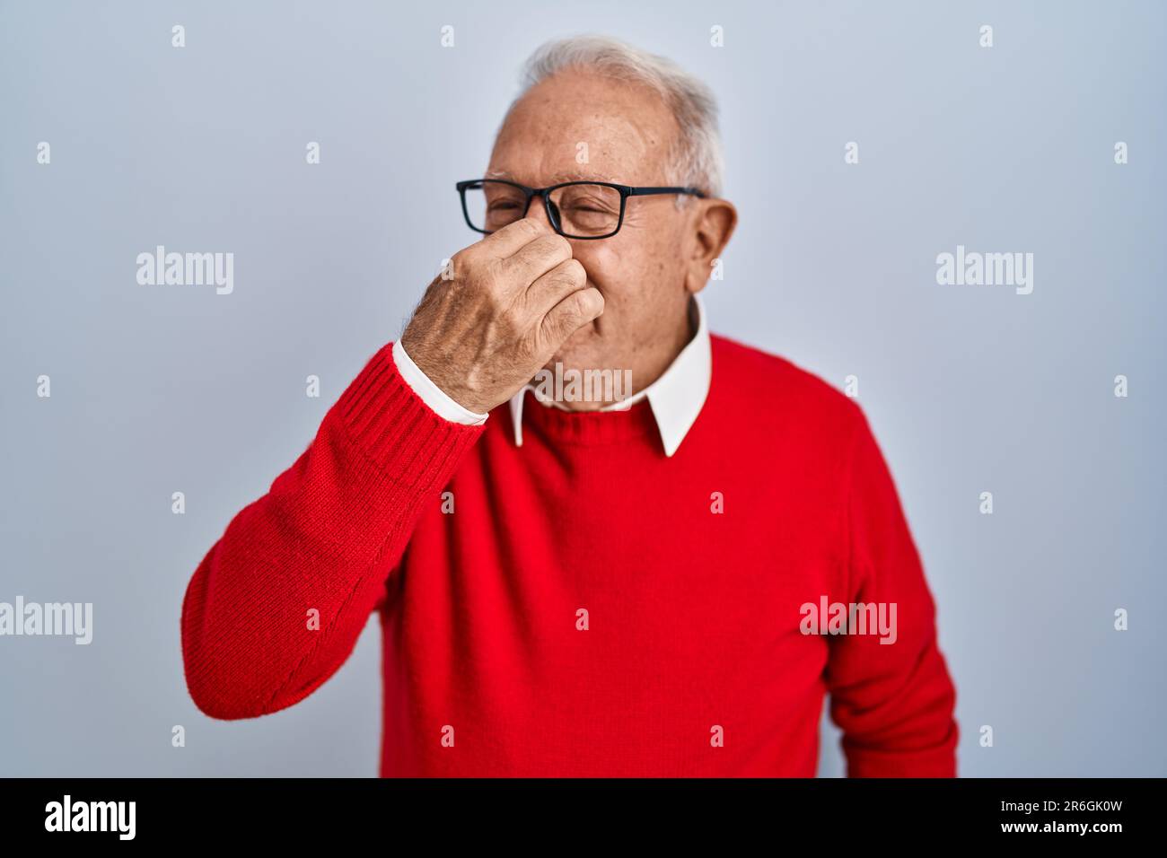 Senior man with grey hair standing over isolated background smelling ...