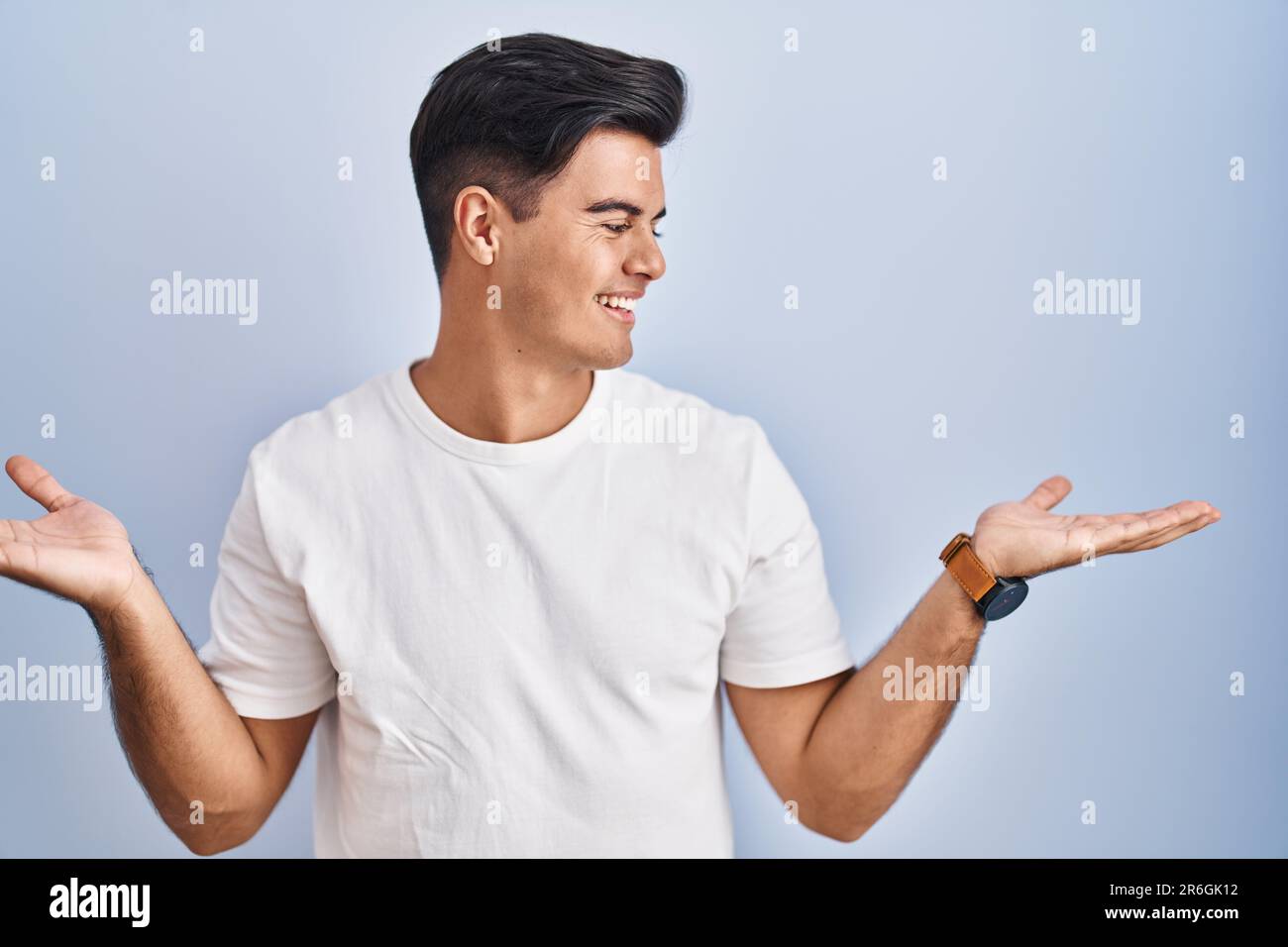 Hispanic man standing over blue background smiling showing both hands ...