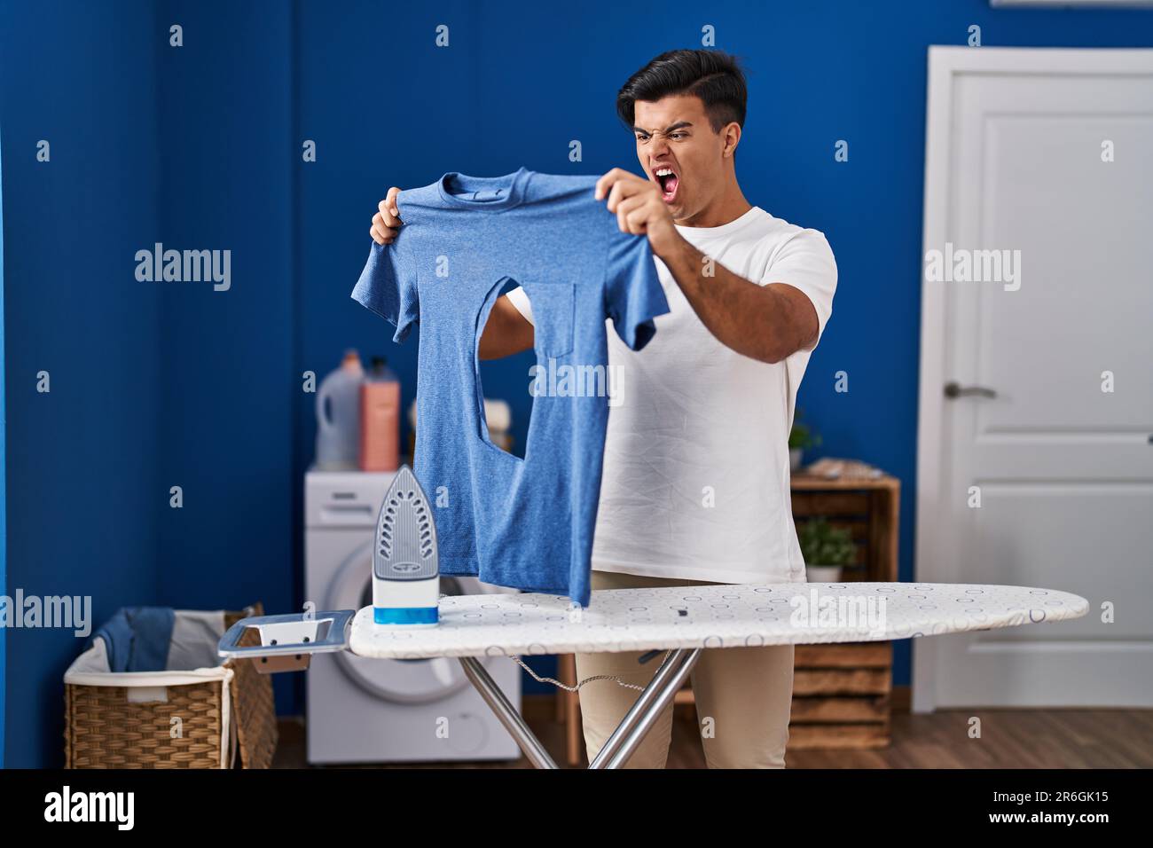 Hispanic man ironing holding burned iron shirt at laundry room angry ...