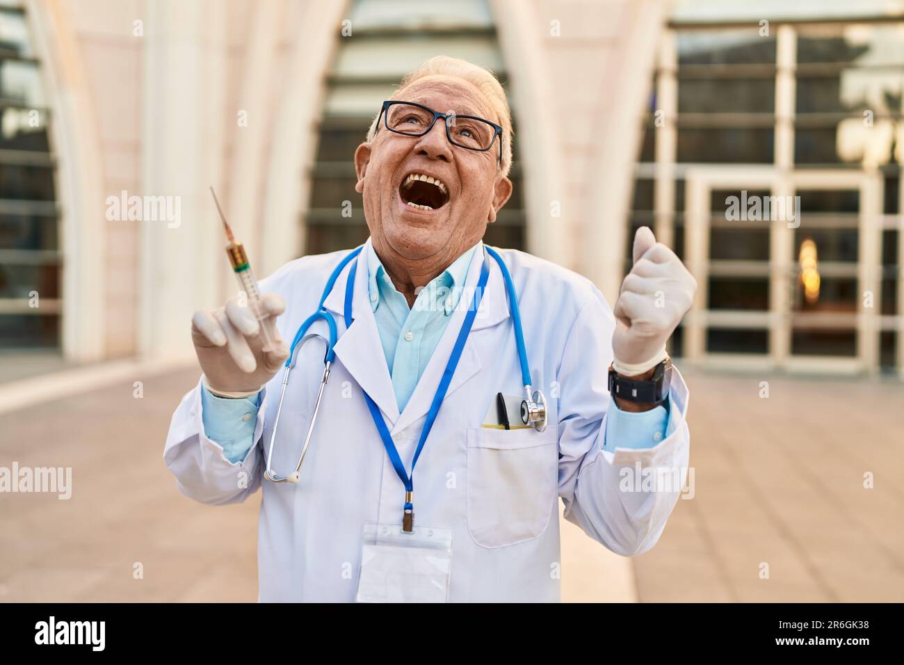 Senior doctor with grey hair holding syringe screaming proud ...