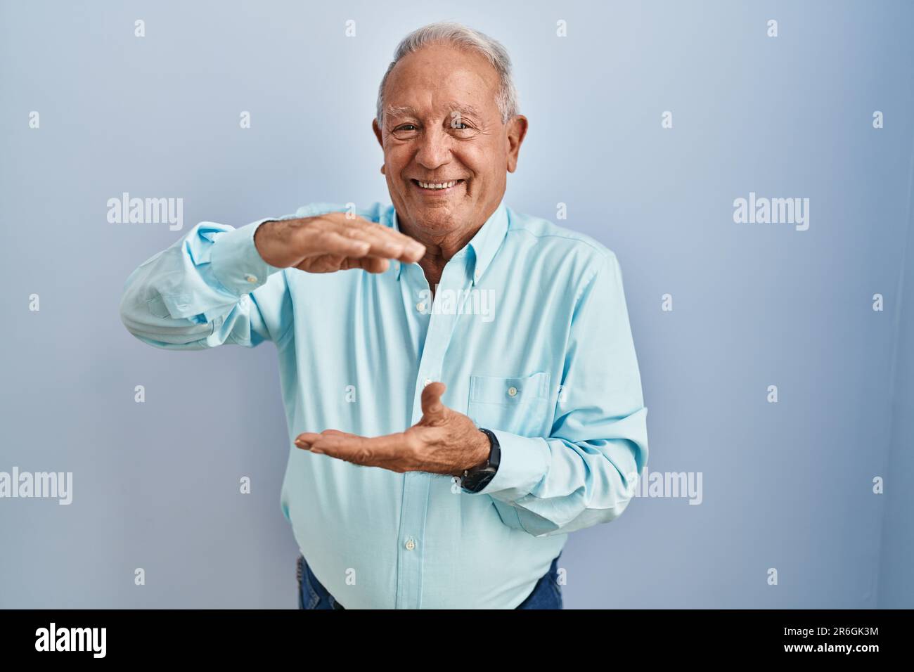 Senior man with grey hair standing over blue background gesturing with ...